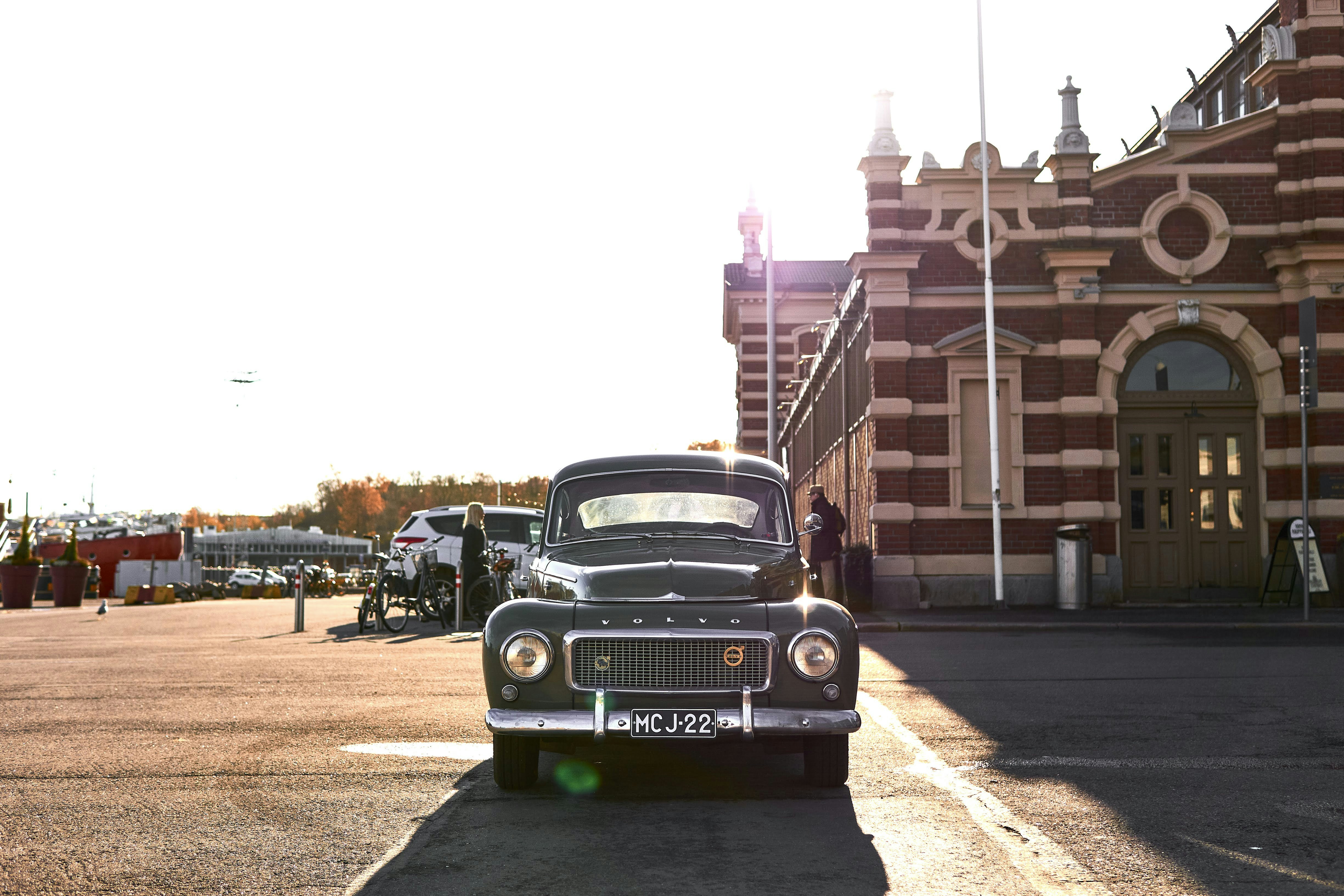 Classic car parked in front of a historic building, bathed in warm sunlight. The scene highlights the contrast between old and new architecture.