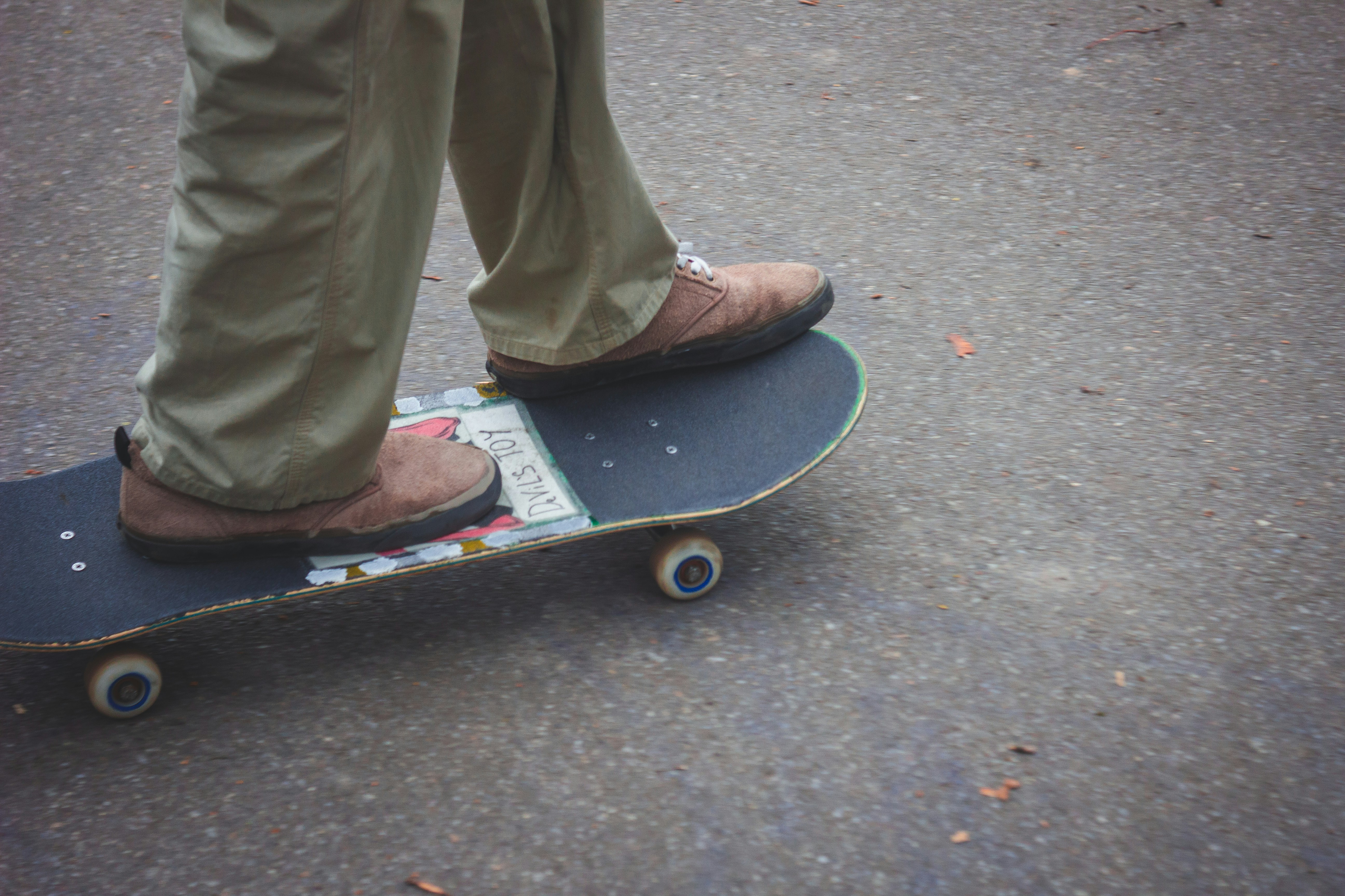 Close-up of a skateboarder’s feet as they ride on a smooth pavement, showcasing the dynamic motion and casual style of urban skating.