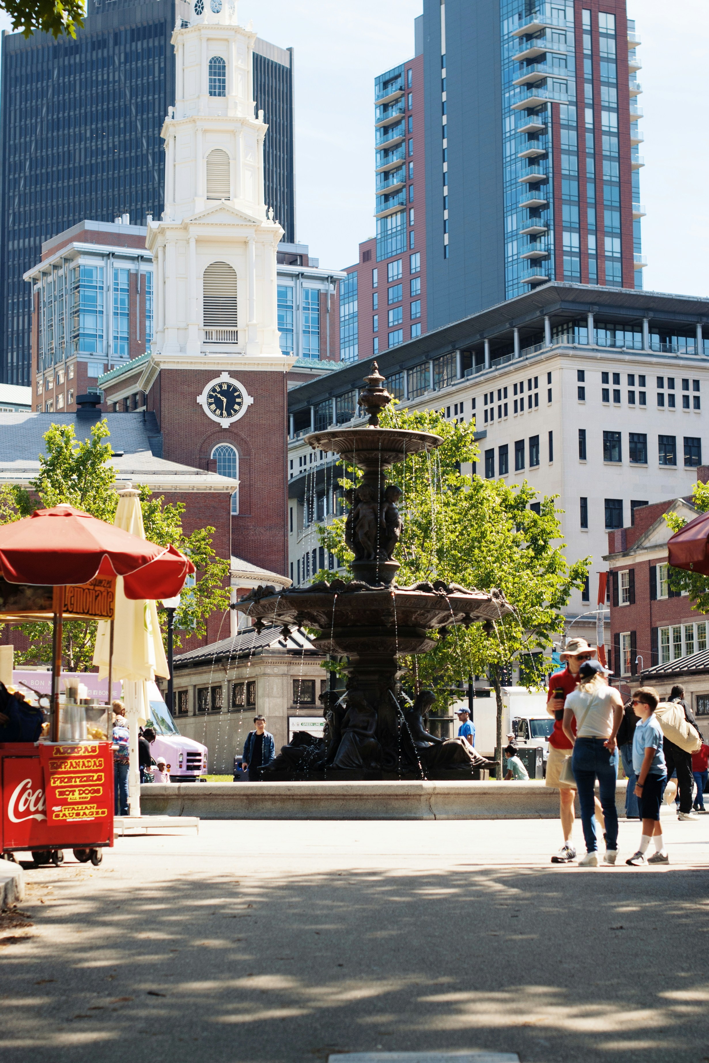 Fountain at the Heart of a Sunlit City Square, Framed by Clock Tower and Glass Giants