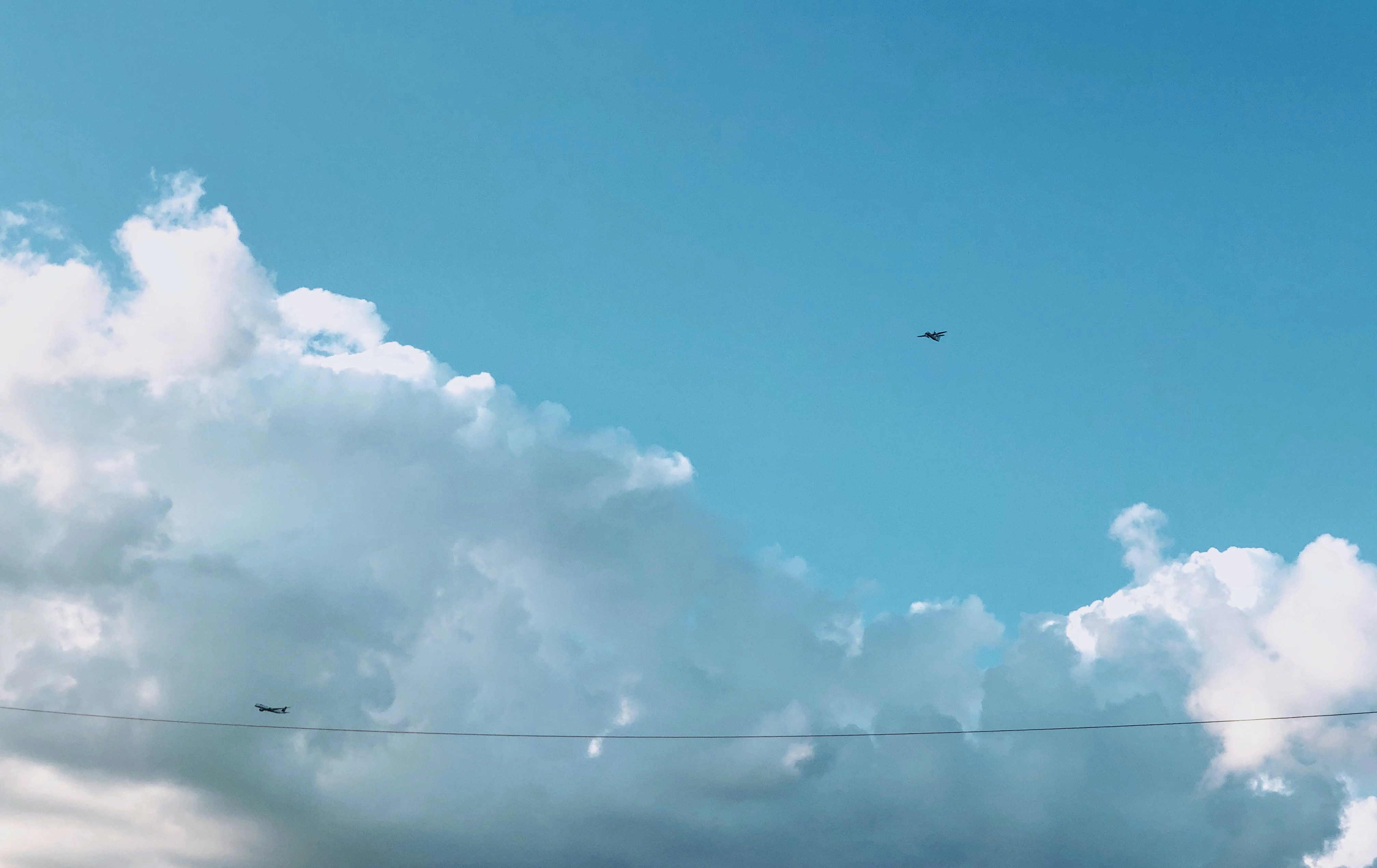 Two aircraft glide through a vast blue sky dotted with fluffy clouds, showcasing the contrast between man-made flight and nature's beauty.
