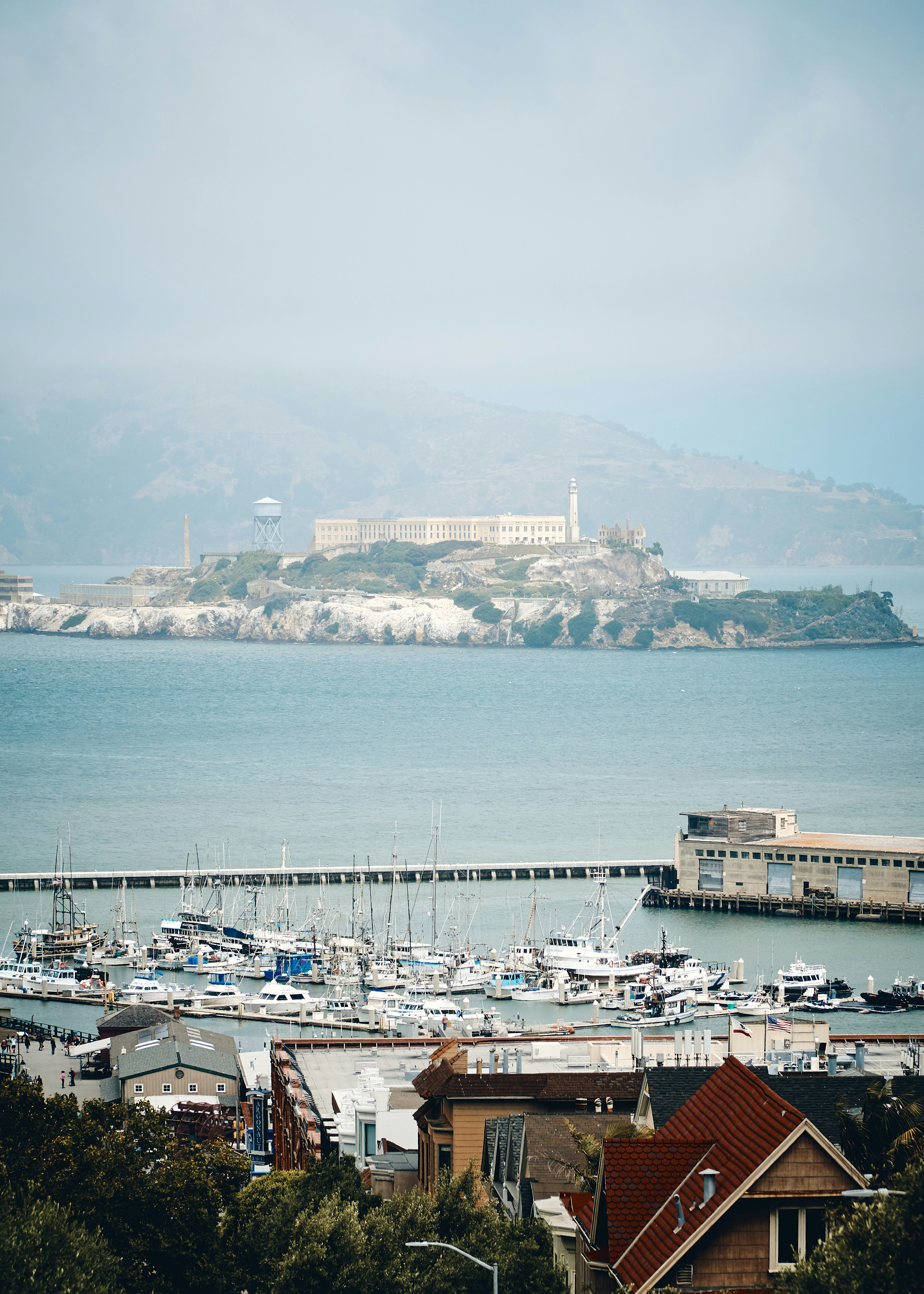 Harbor with moored boats and distant island fortress under a cloudy sky.