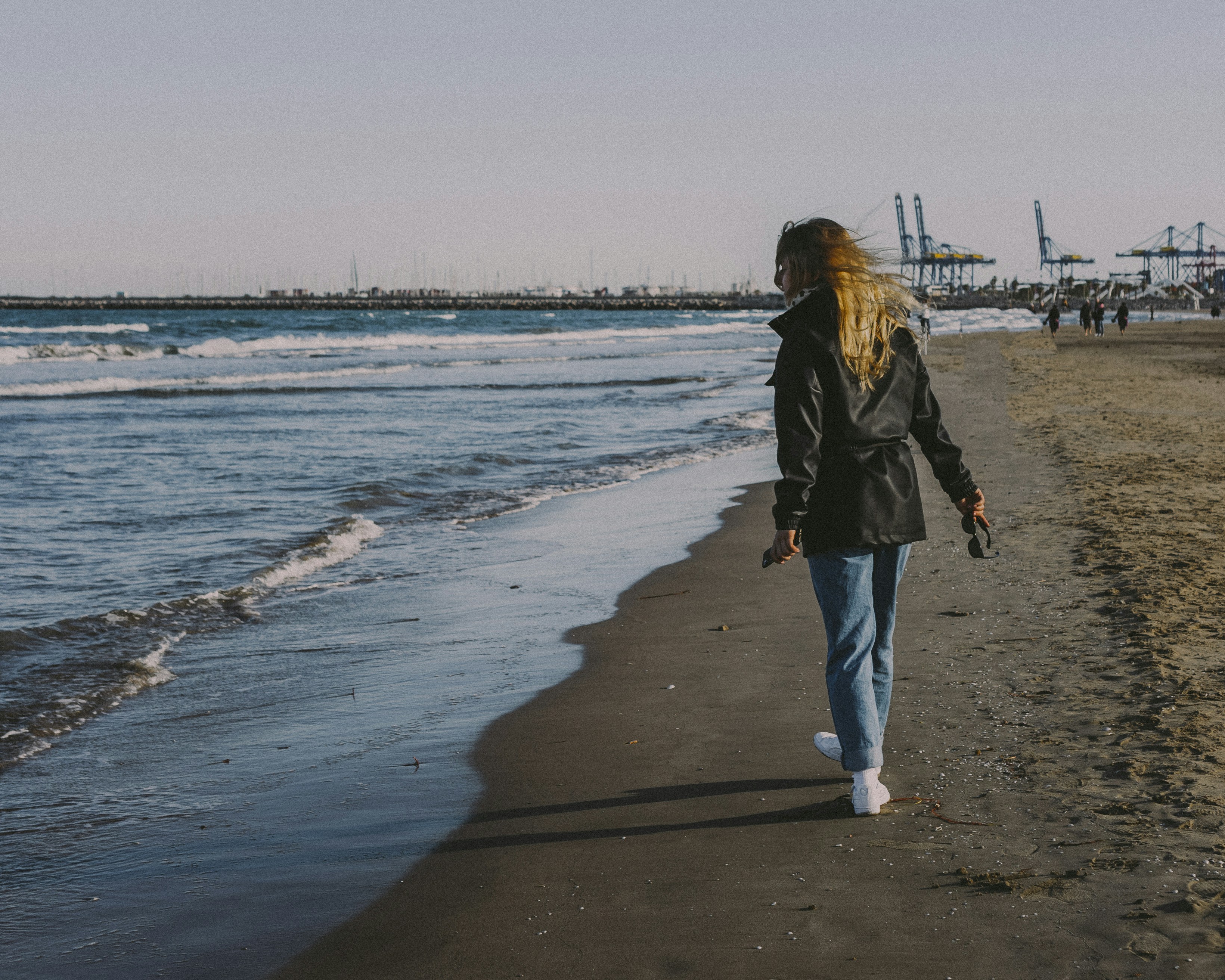 Coastal Stroll: Woman in a Windy Shoreline Walk