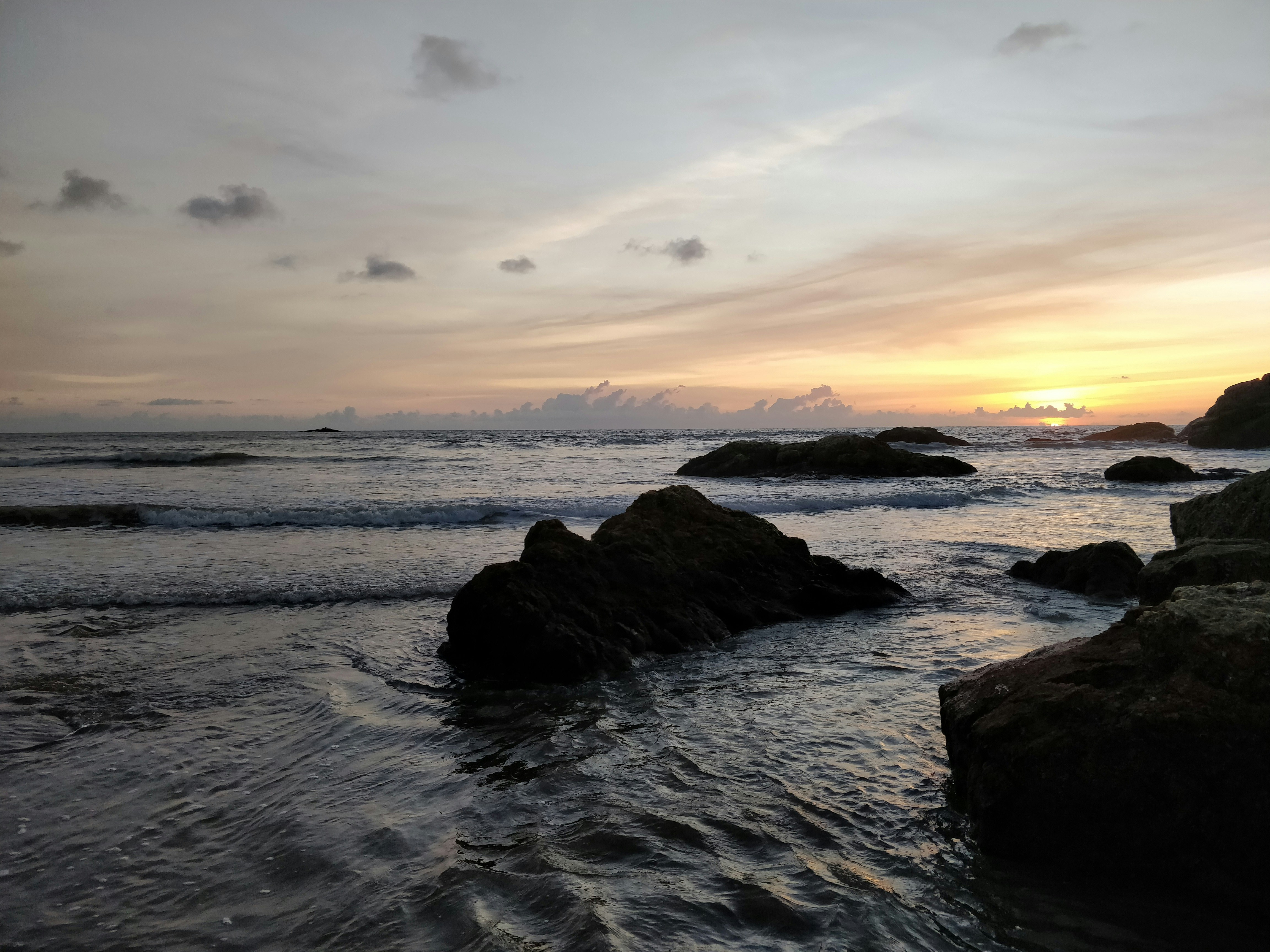 Ocean waves gently lap against dark rocks under a serene sunset sky.