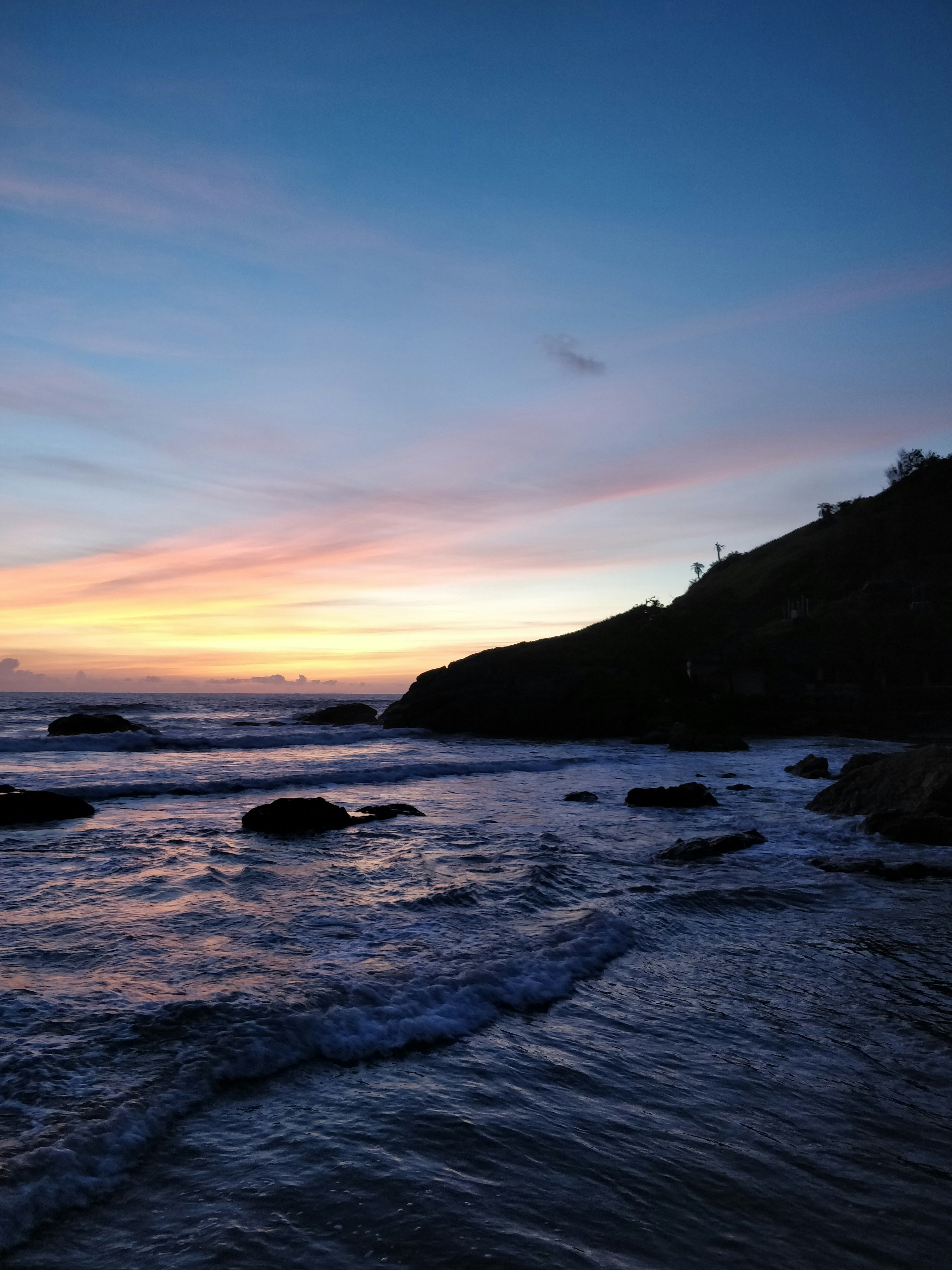 Ocean waves gently lap against a rocky coastline under a vibrant sunset sky.