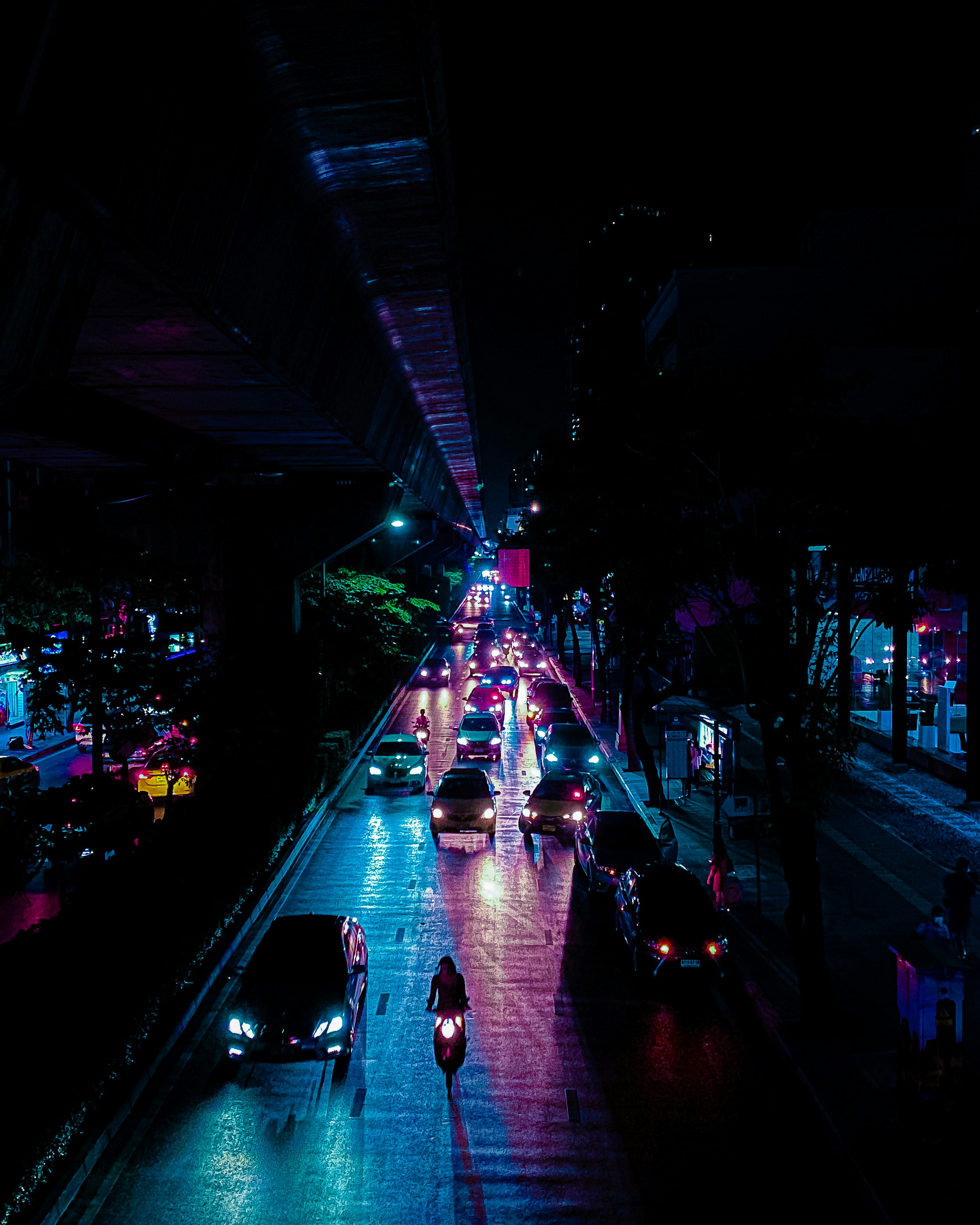 Vibrant city street illuminated by neon lights, featuring moving vehicles and a motorcycle amidst a bustling urban environment.
