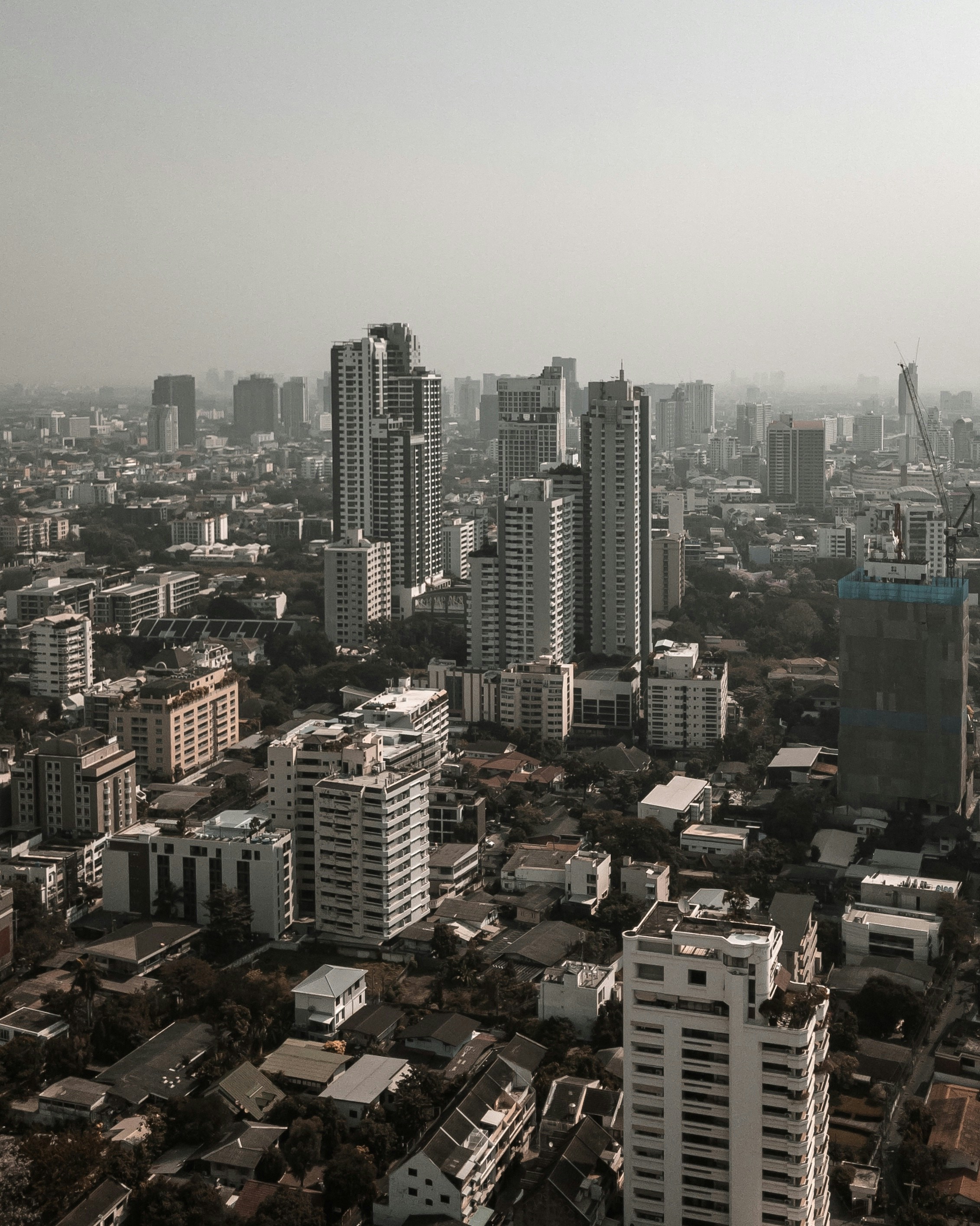 Aerial view of a bustling cityscape featuring a mix of high-rise buildings and residential areas, showcasing urban development amidst a hazy backdrop.