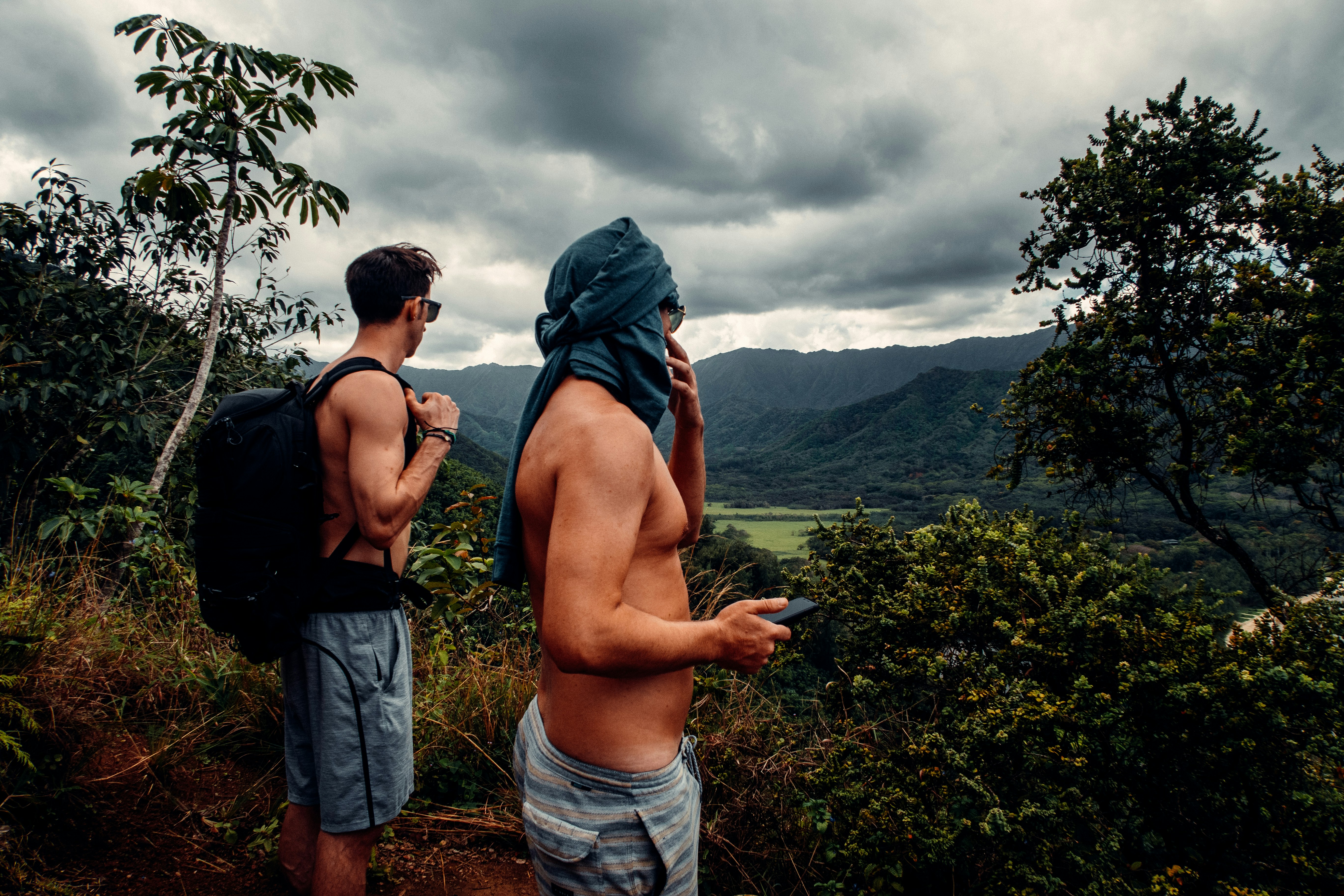Two hikers overlook a lush valley from a rocky vantage at dusk