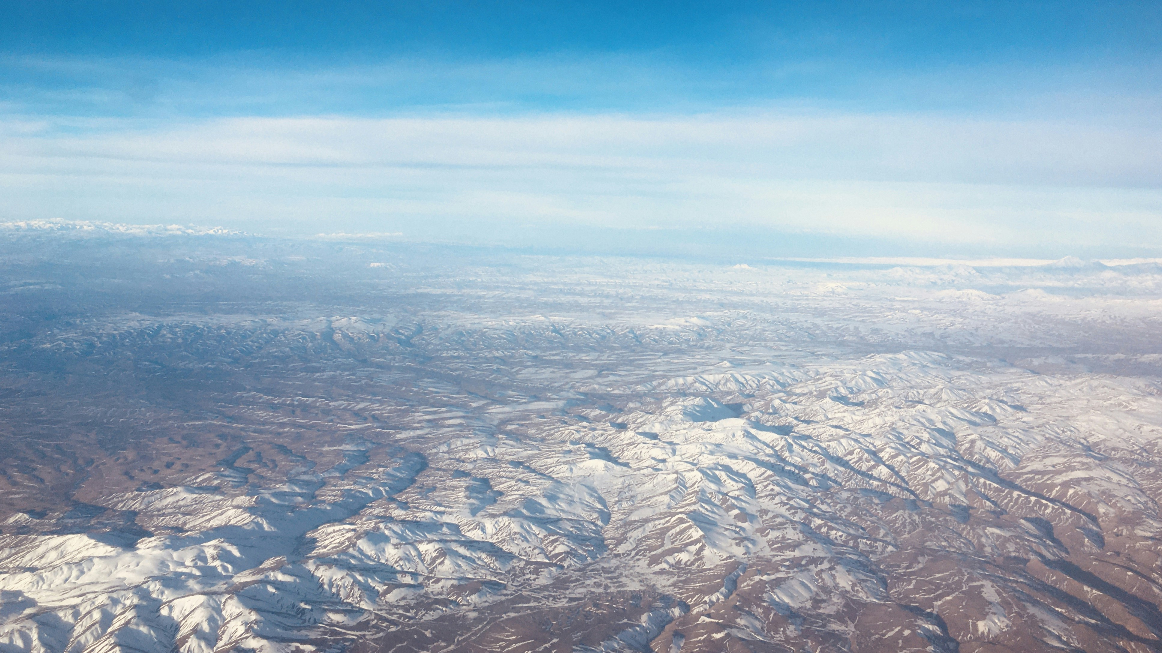 Expansive landscape of rugged terrain with snow patches under a clear blue sky.