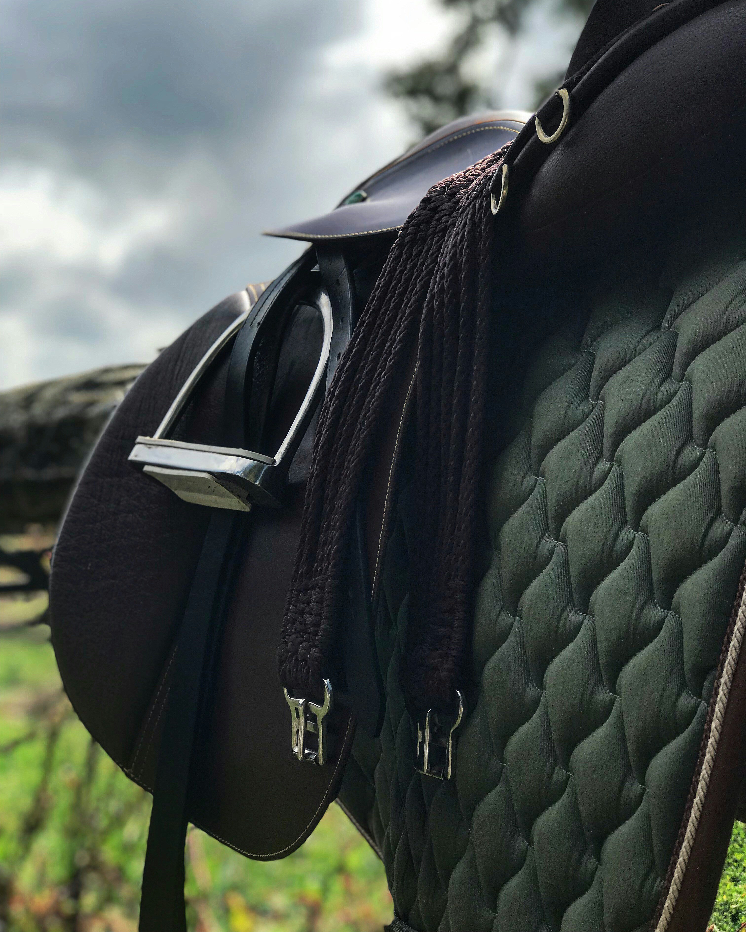 Close-up of a richly textured saddle and saddle pad, showcasing intricate stitching and materials. Natural light accentuates the craftsmanship and details.