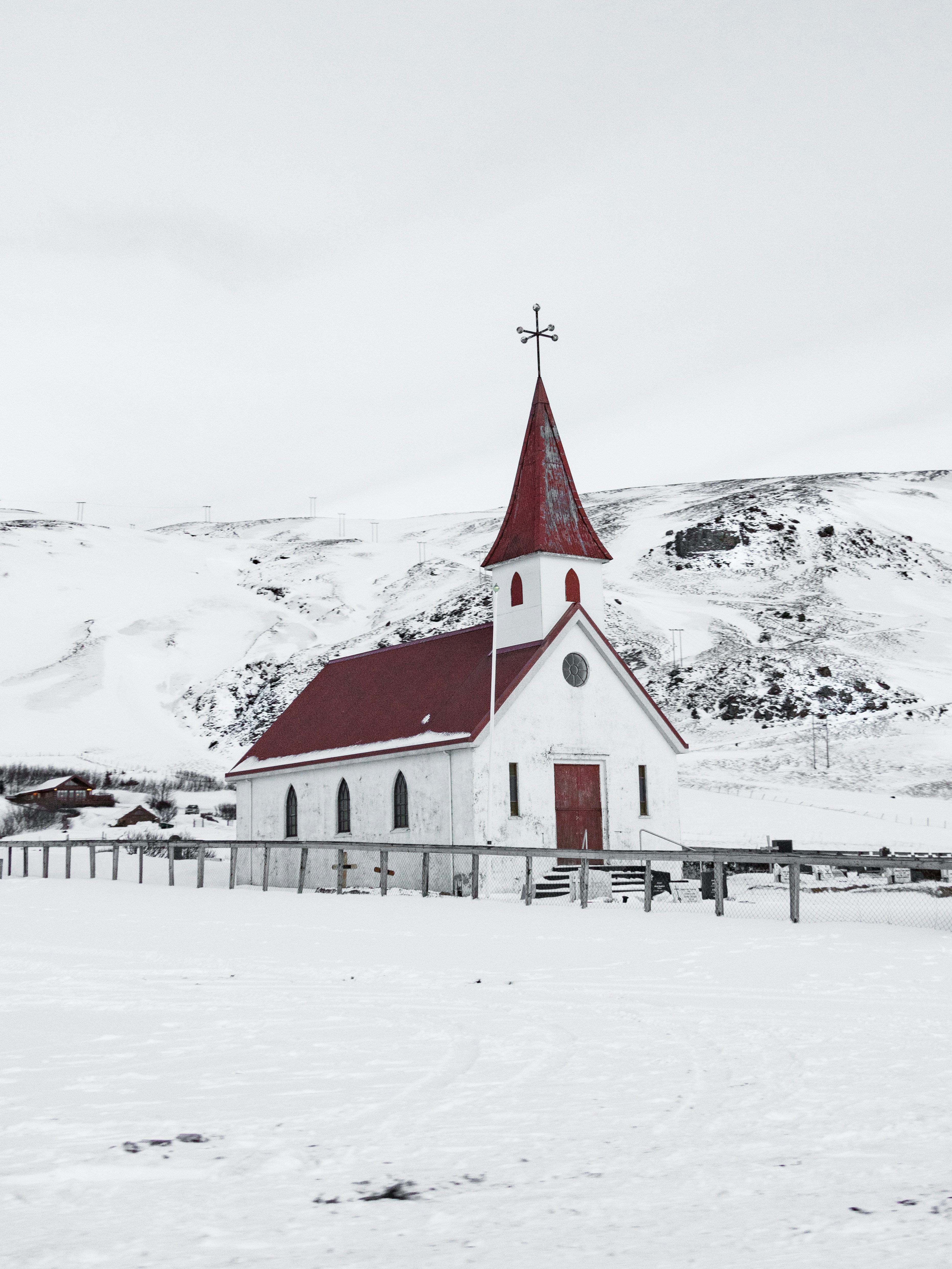 A quaint white church with a red roof stands alone in a snowy landscape, surrounded by rolling hills. The serene atmosphere evokes a sense of peace and solitude.