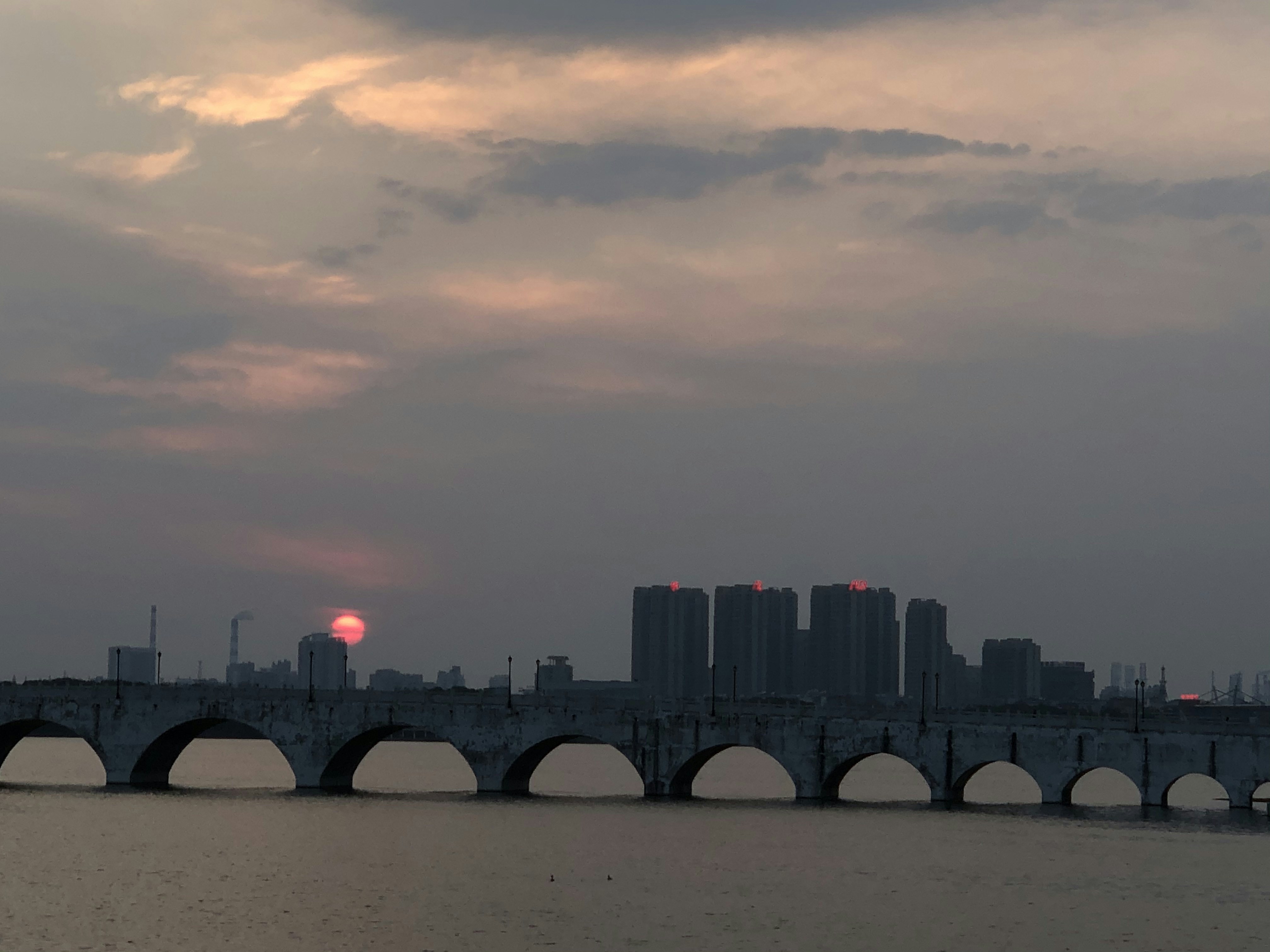 Silhouette of a bridge against a dimly lit city skyline during sunset.