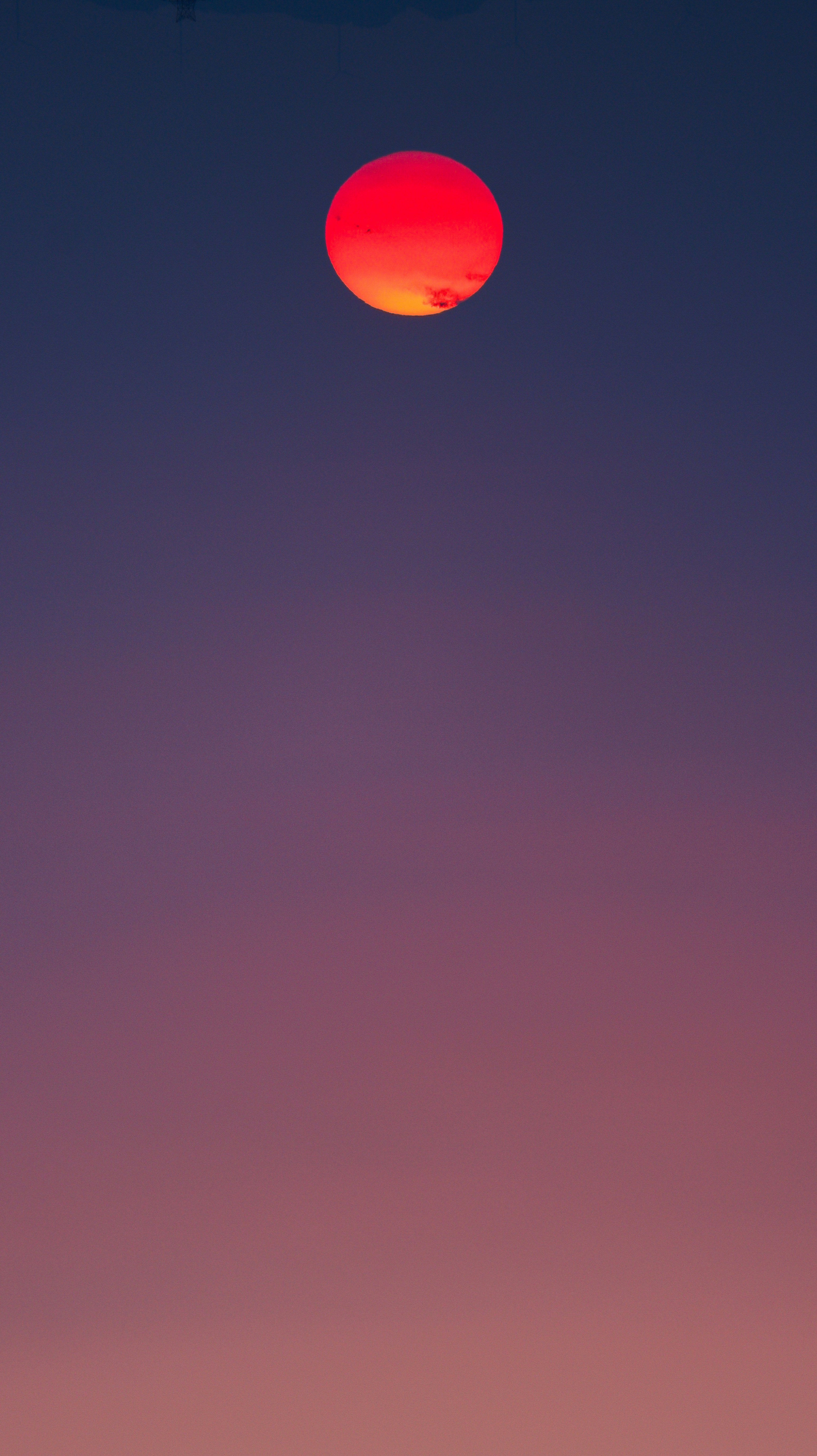 Vibrant sun setting against a gradient sky, transitioning from deep blue to soft pink hues. A serene moment capturing the day's end.