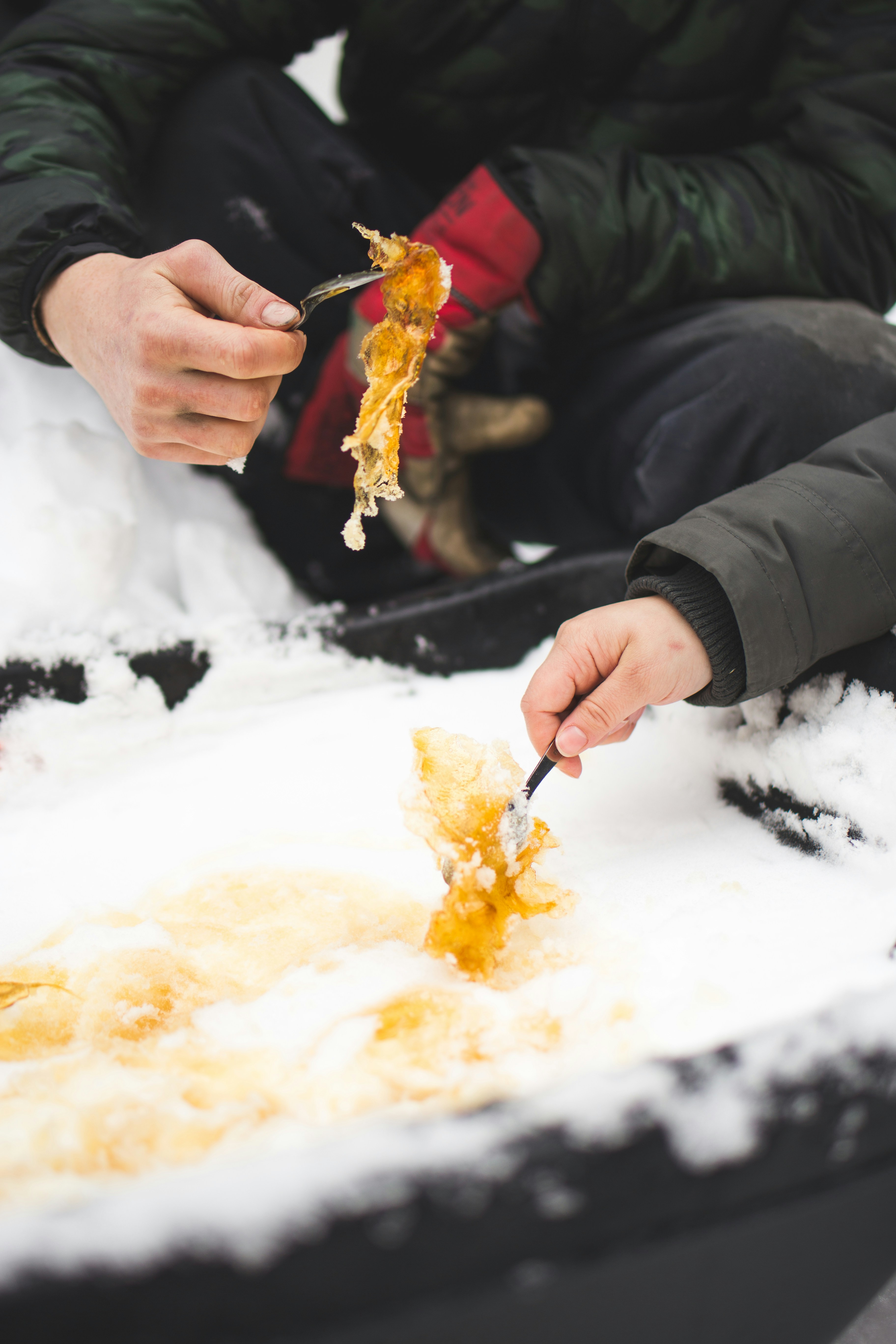 Two hands scoop golden syrup from a snow-filled container, capturing a unique winter treat experience.