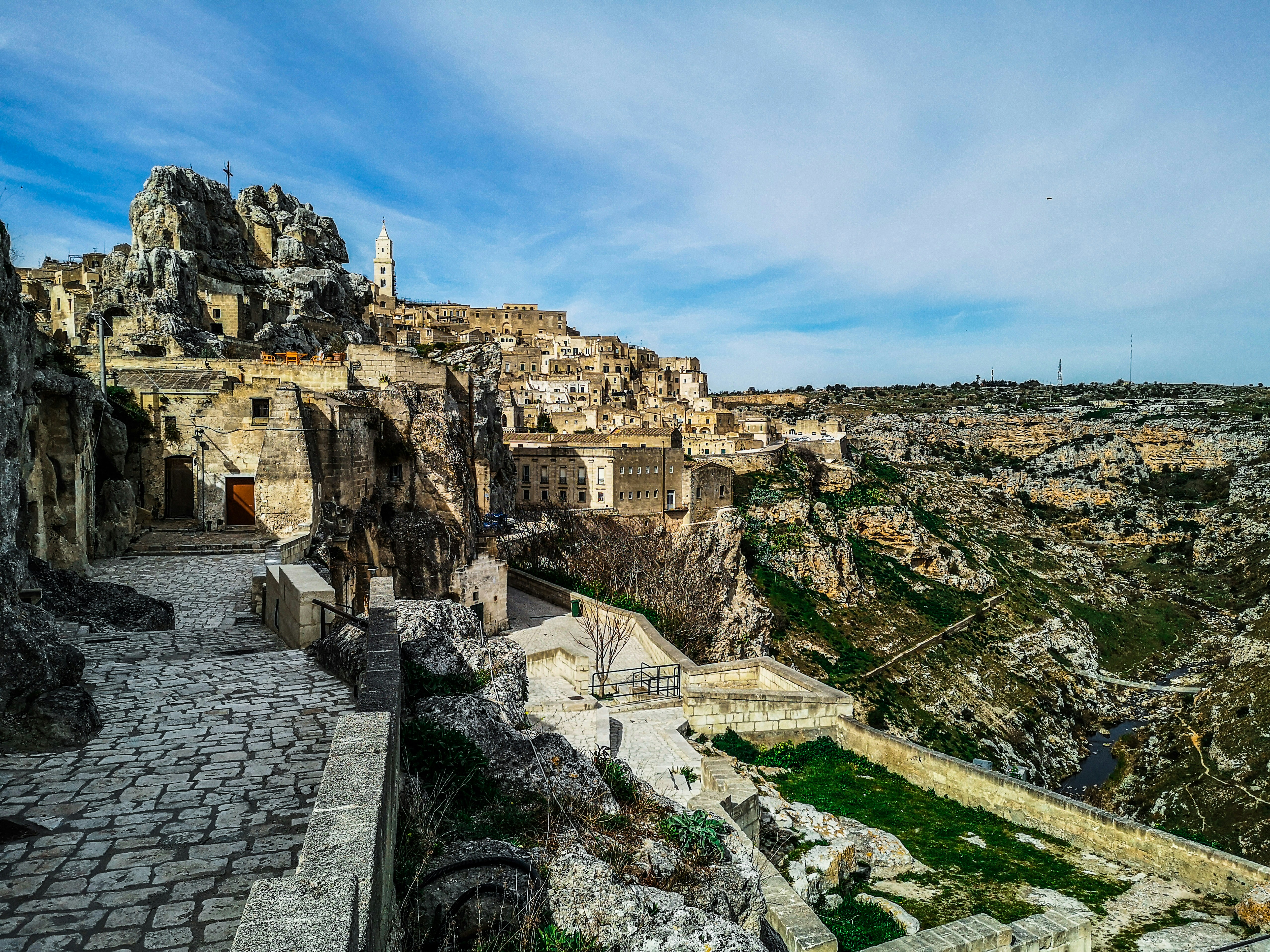 Historic stone buildings nestled against rugged cliffs under a vast blue sky.