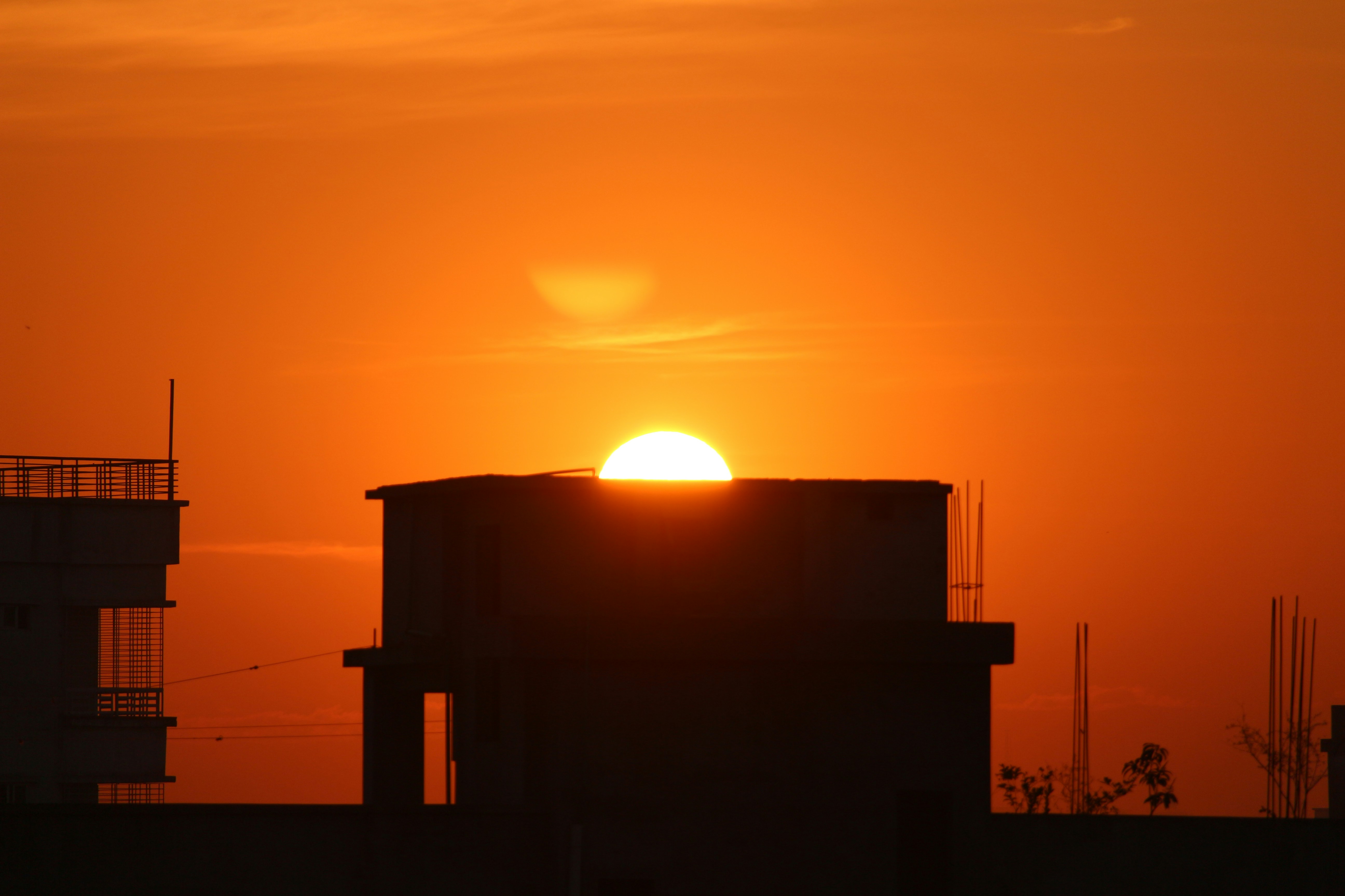 Sun rising behind silhouetted buildings against an orange sky.