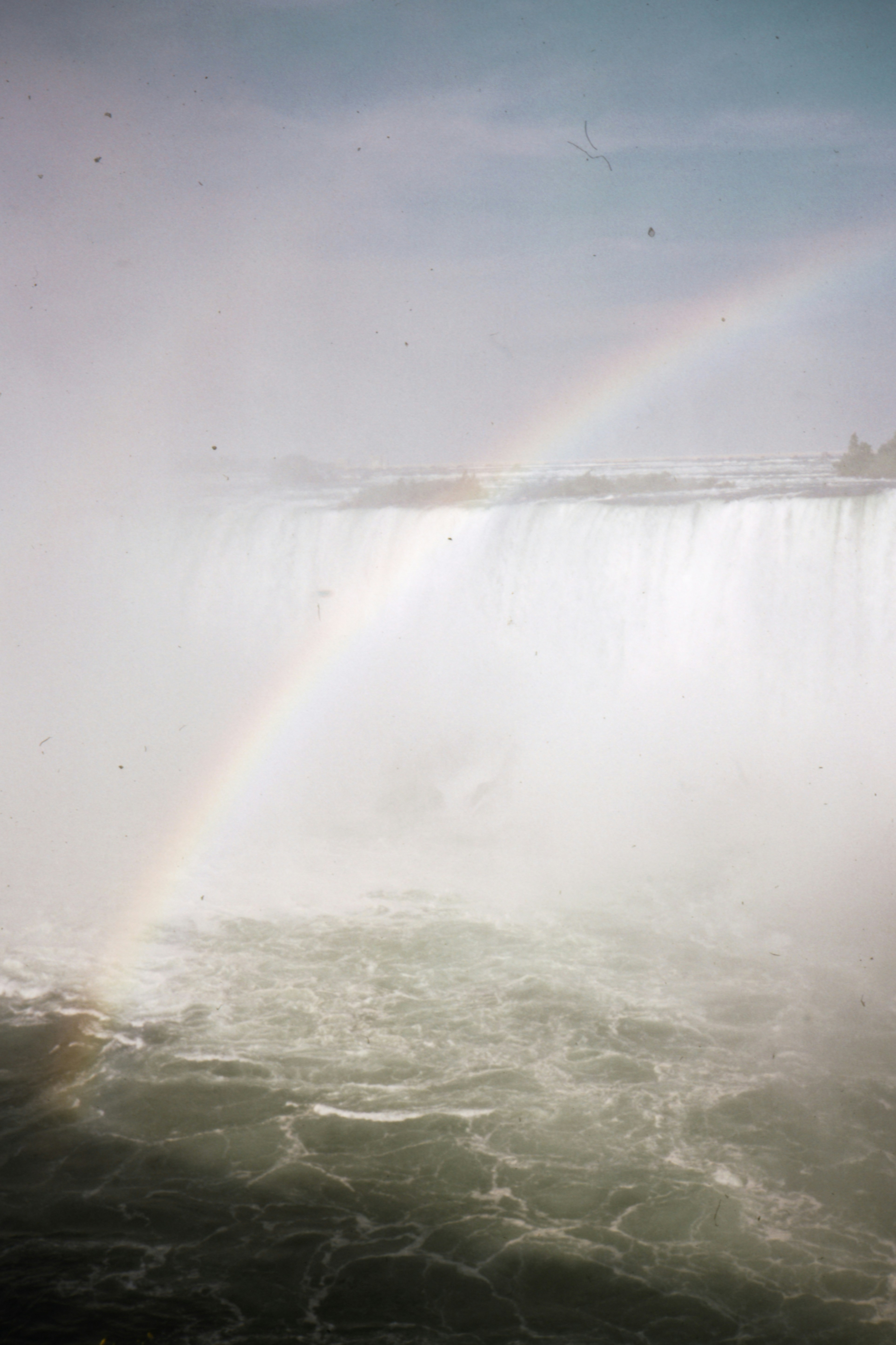 A vibrant rainbow arcs gracefully over the cascading waters of a majestic waterfall, enveloped in mist and sunlight.