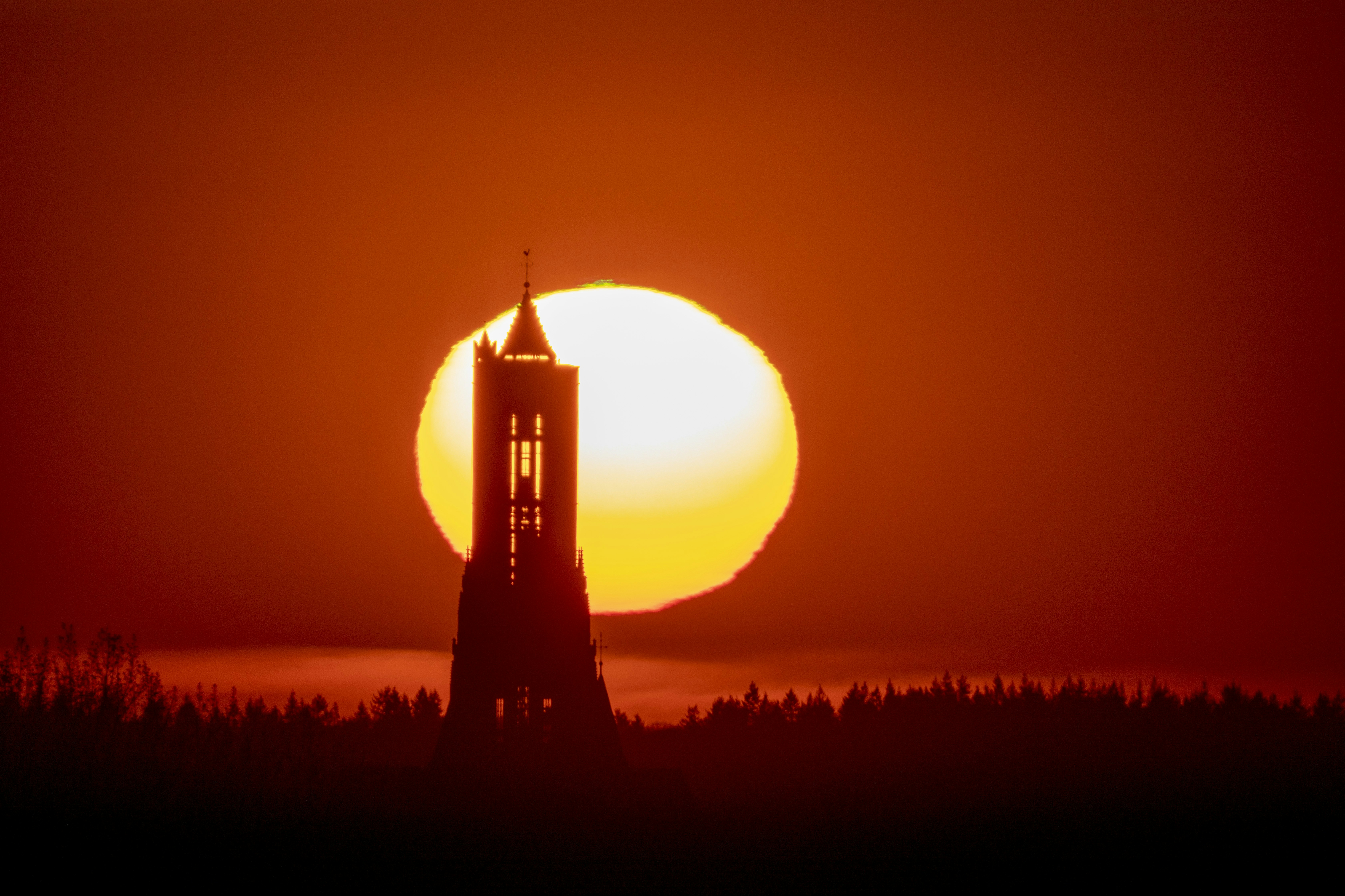 Tower silhouette framed by a large, glowing sunset, creating a dramatic contrast against the darkening landscape.