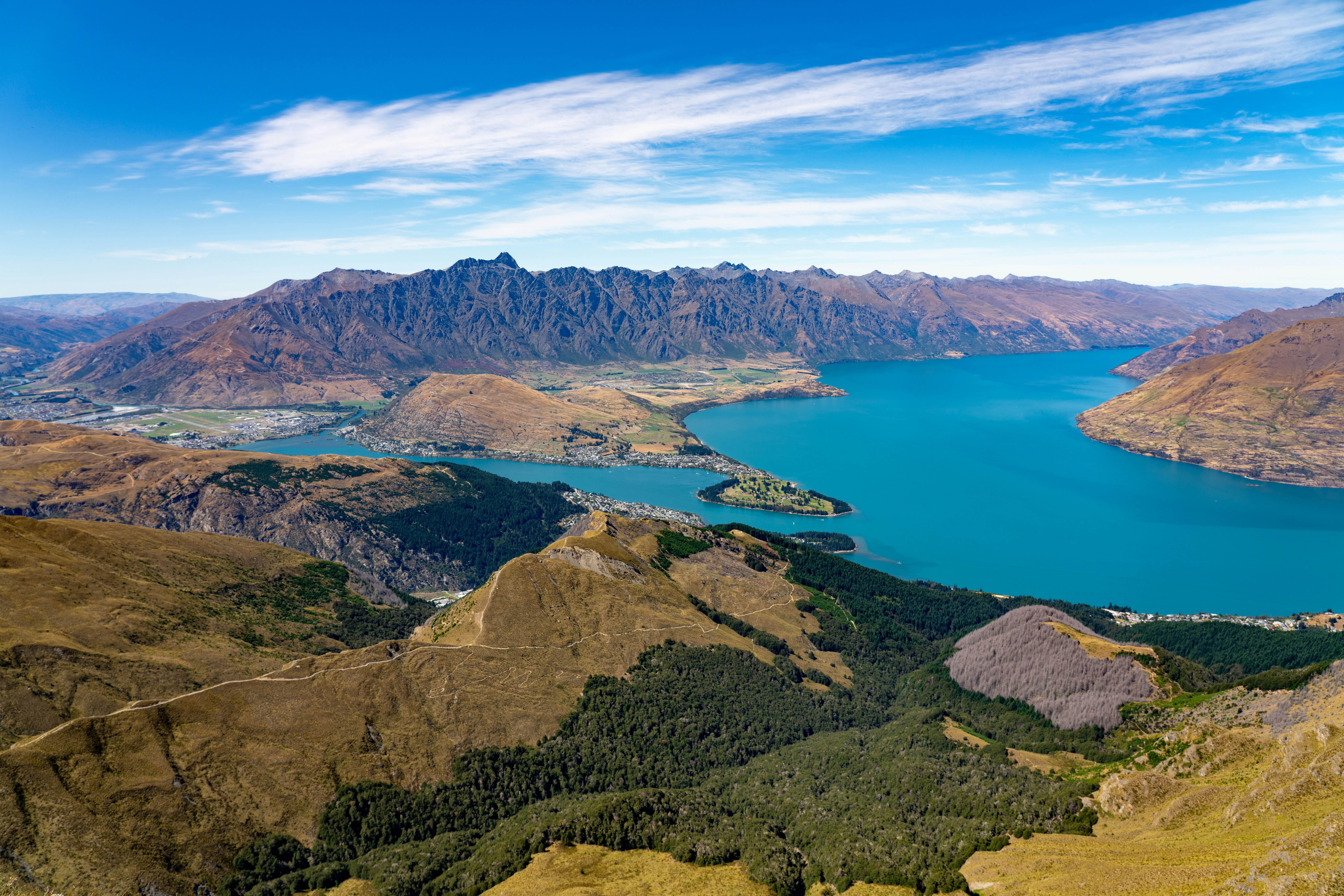 Expansive view of Lake Wakatipu with surrounding mountains under a bright blue sky.