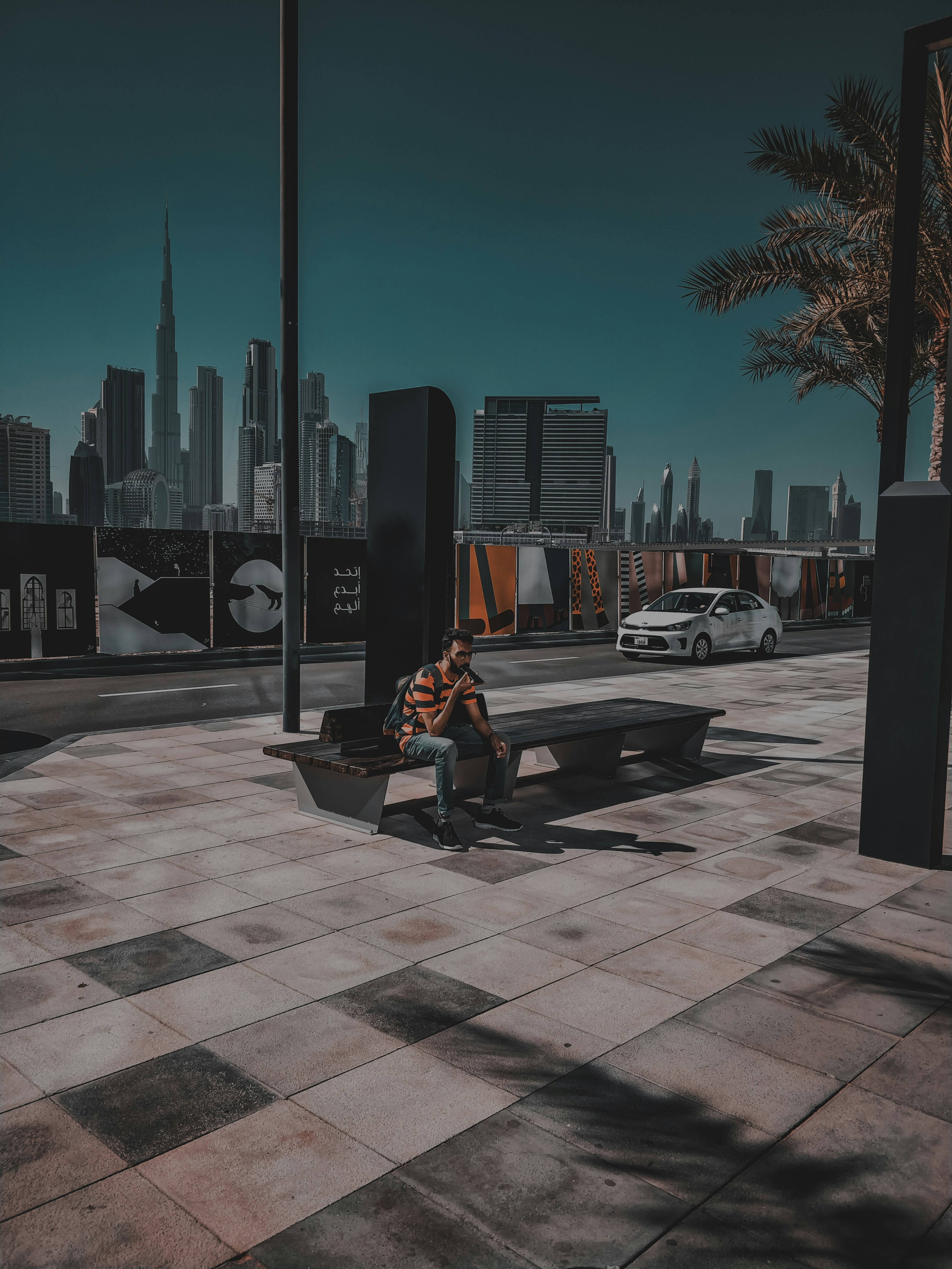 man in black jacket sitting on bench near cars during daytime