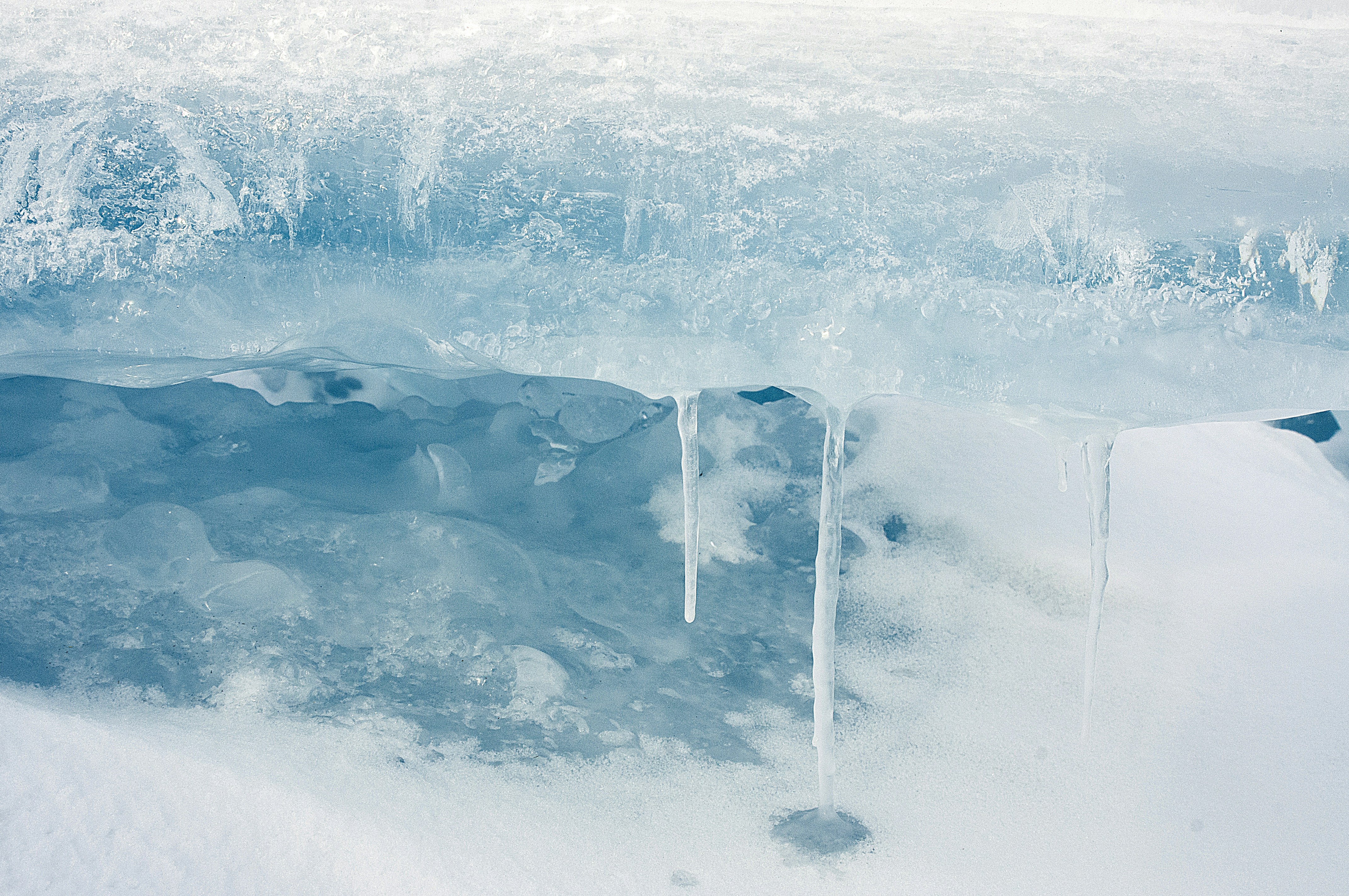 Close-up of crystalline ice formations with delicate icicles hanging, showcasing the intricate textures of winter's grip on a landscape.