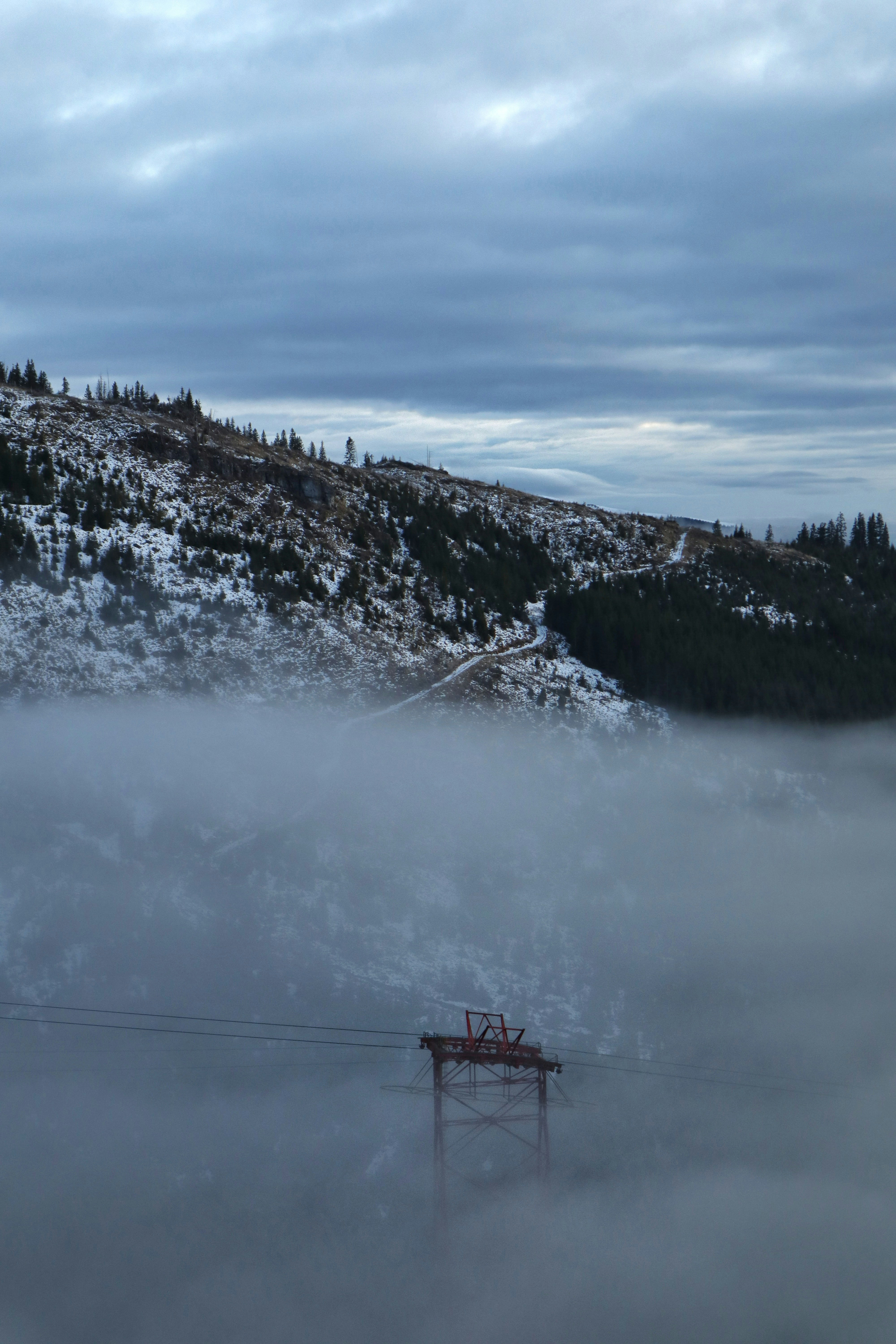Ridge in the Mist: a lone ski-lift pierces the fog above a snow-dusted slope