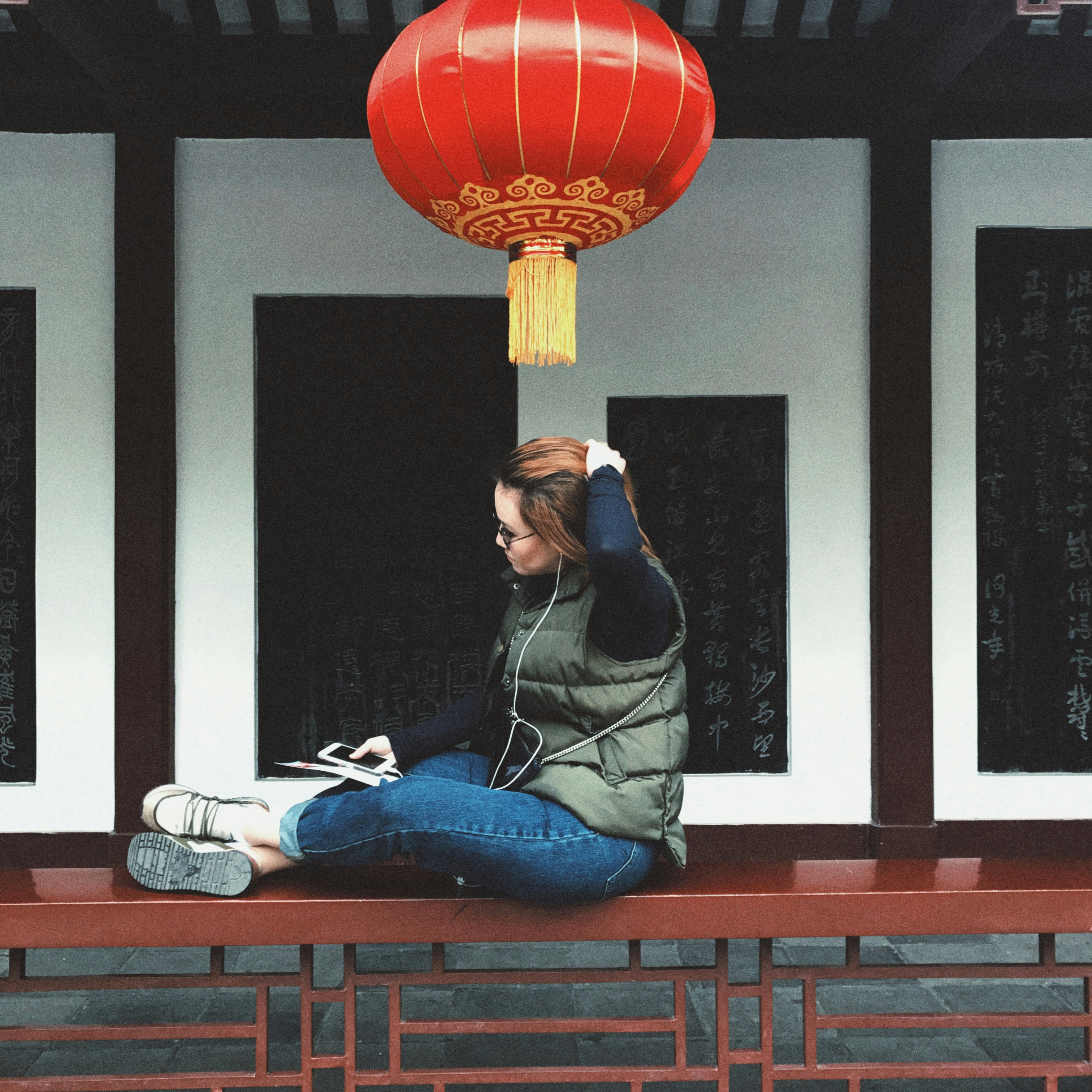 woman in black jacket and blue denim jeans sitting on brown wooden bench