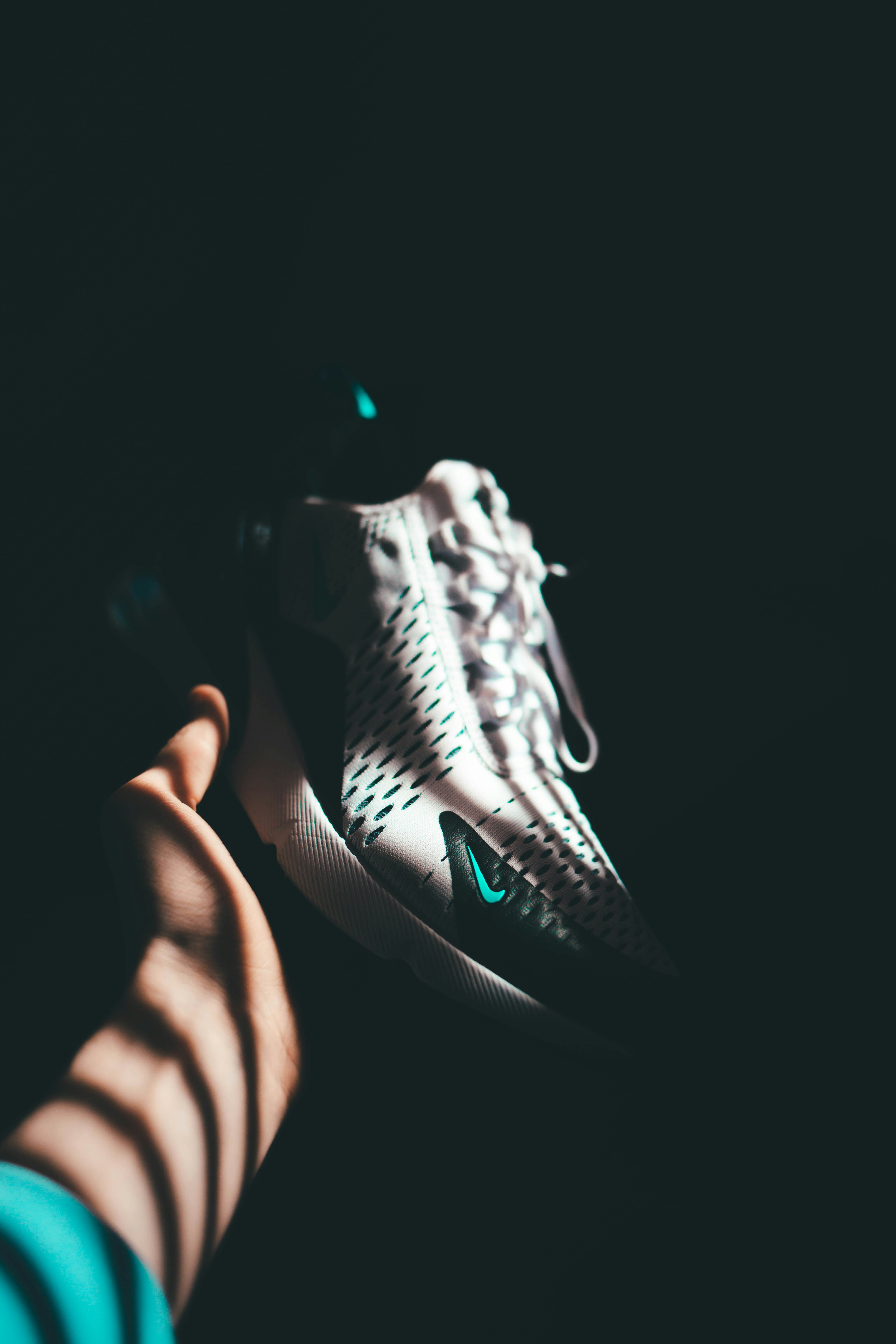 A hand elegantly showcases a modern sneaker, featuring a dynamic design and vibrant accents against a dark backdrop. The interplay of light and shadow enhances its stylish appeal.