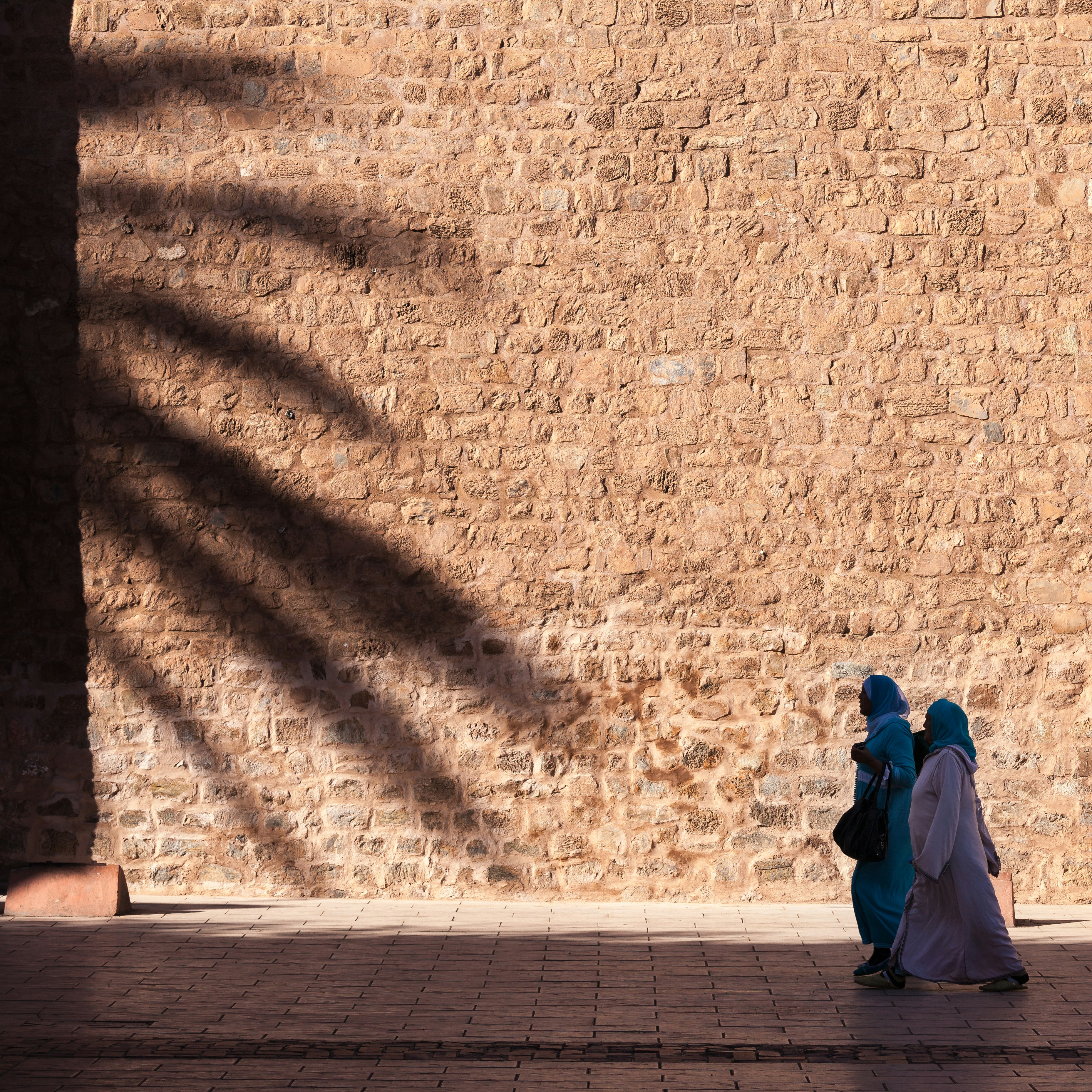 Two Robes, One Shadow: Quiet Passage Along a Sunlit Wall