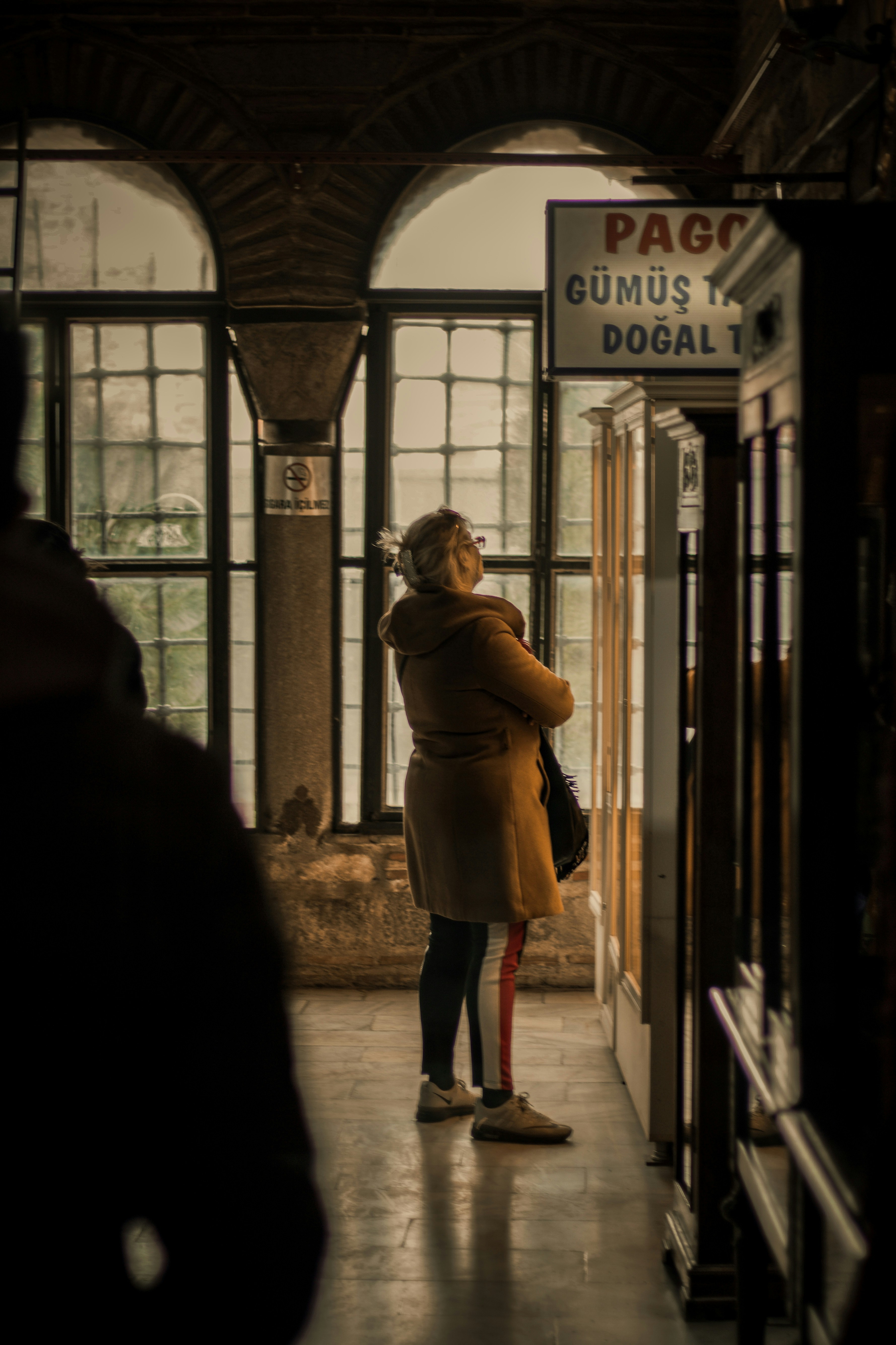 A woman in a cozy coat explores an antique shop, captivated by the displayed items under the warm glow of ambient light.