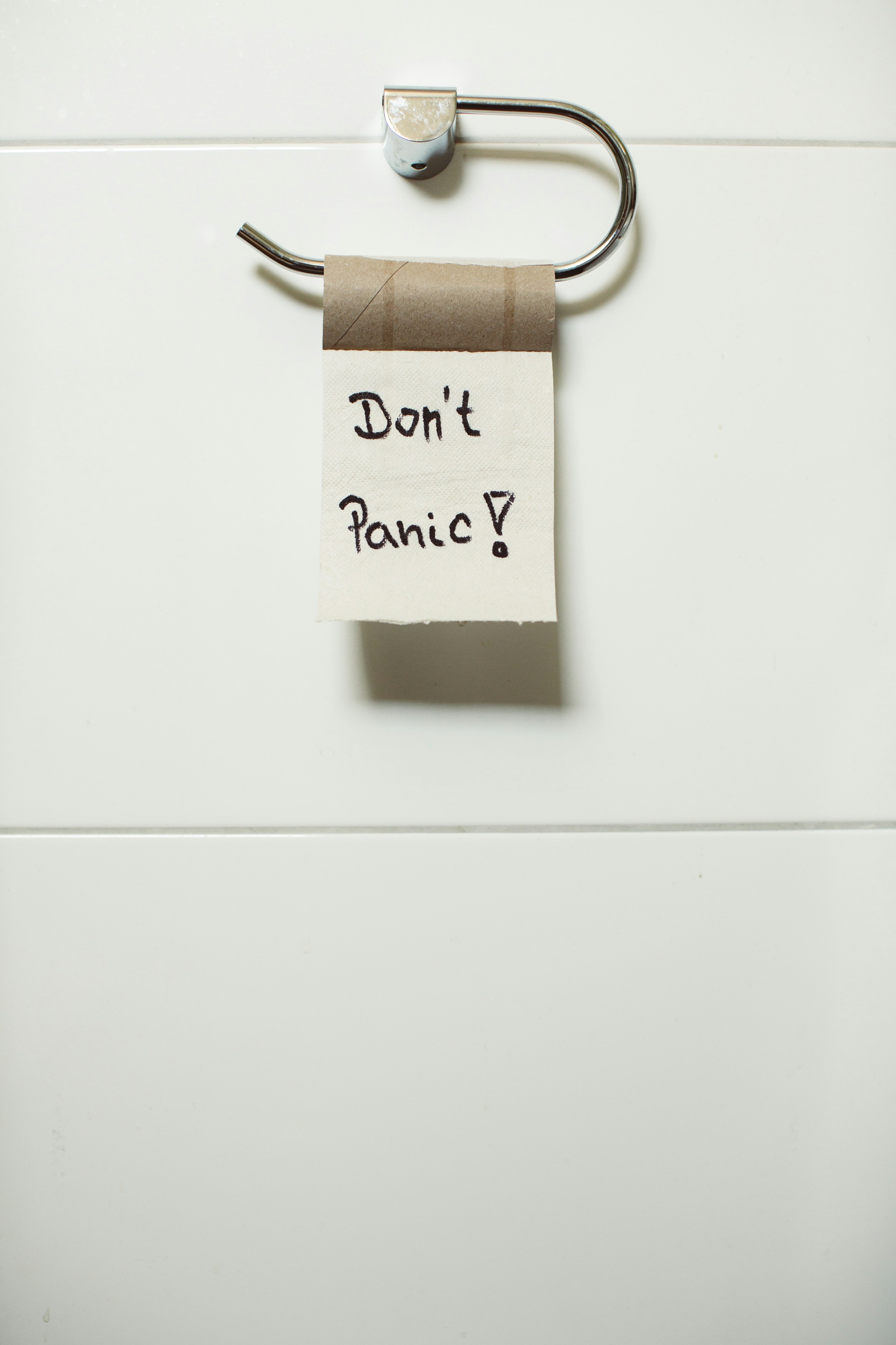 Note with the message 'Don't Panic!' hanging on a wall-mounted holder against a plain background.