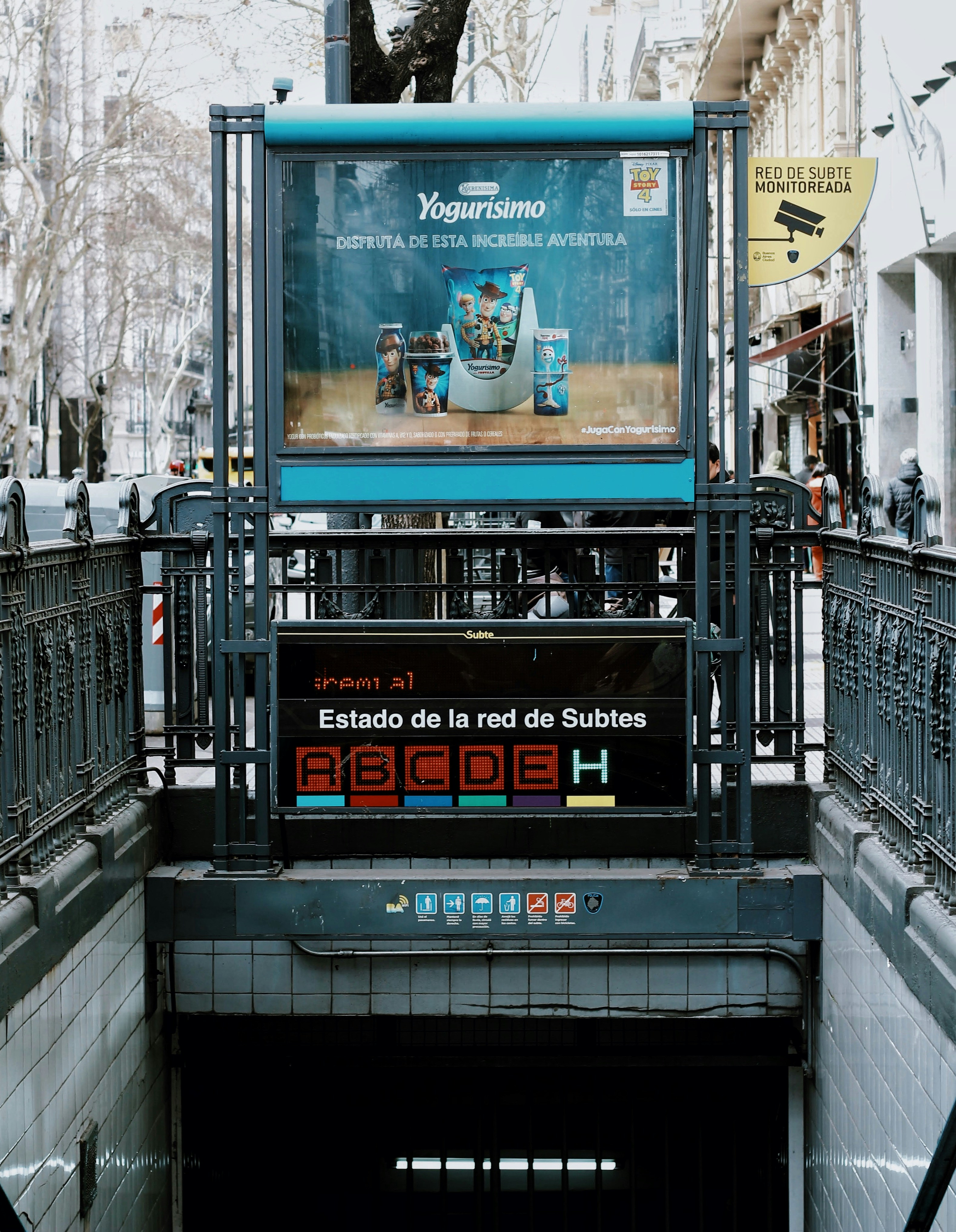 Blue-Framed Advertising Kiosk Over a Subway Entrance Guarded by Iron Railings