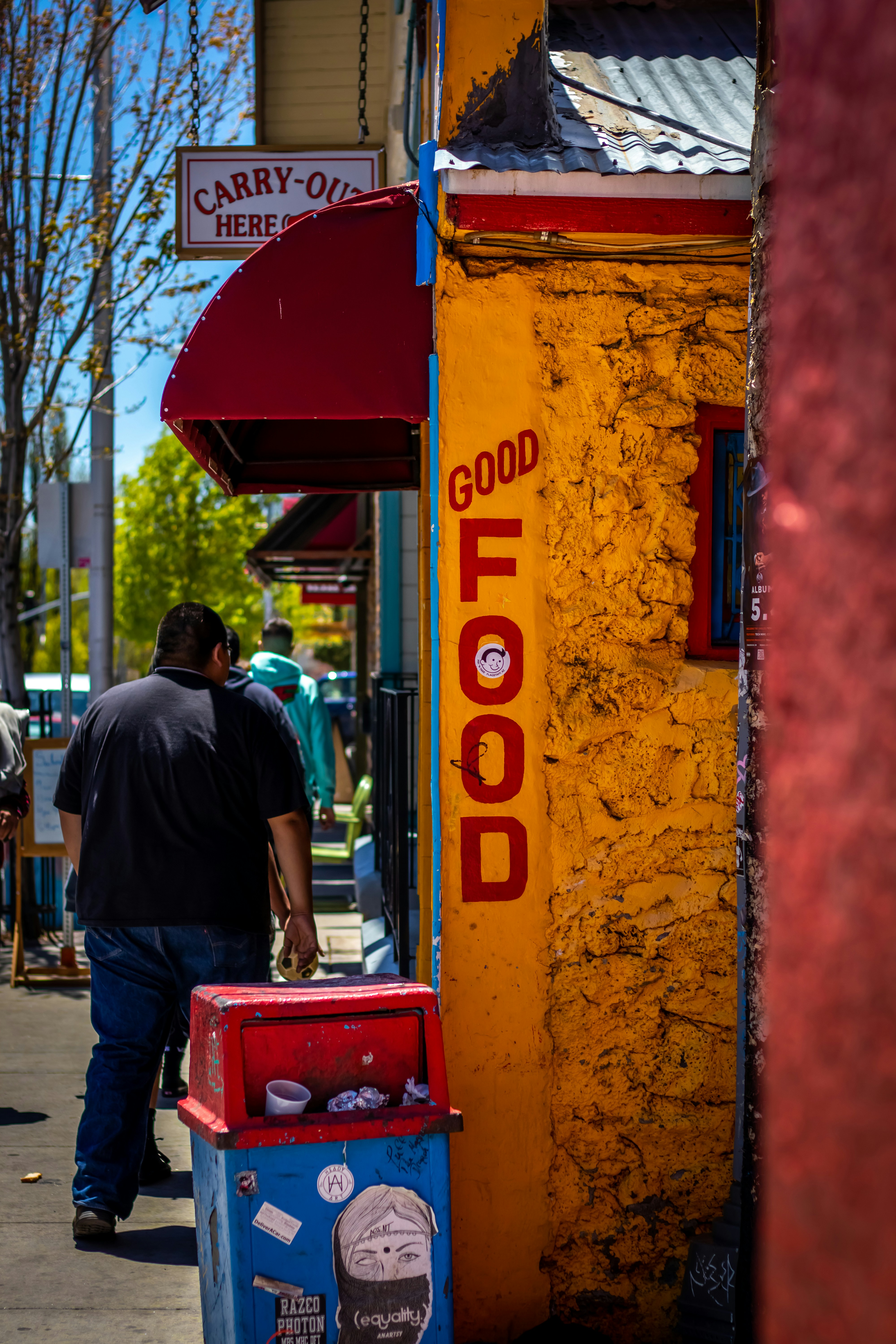 Sunlit Yellow Facade: Lively Street Corner with Good Food Sign