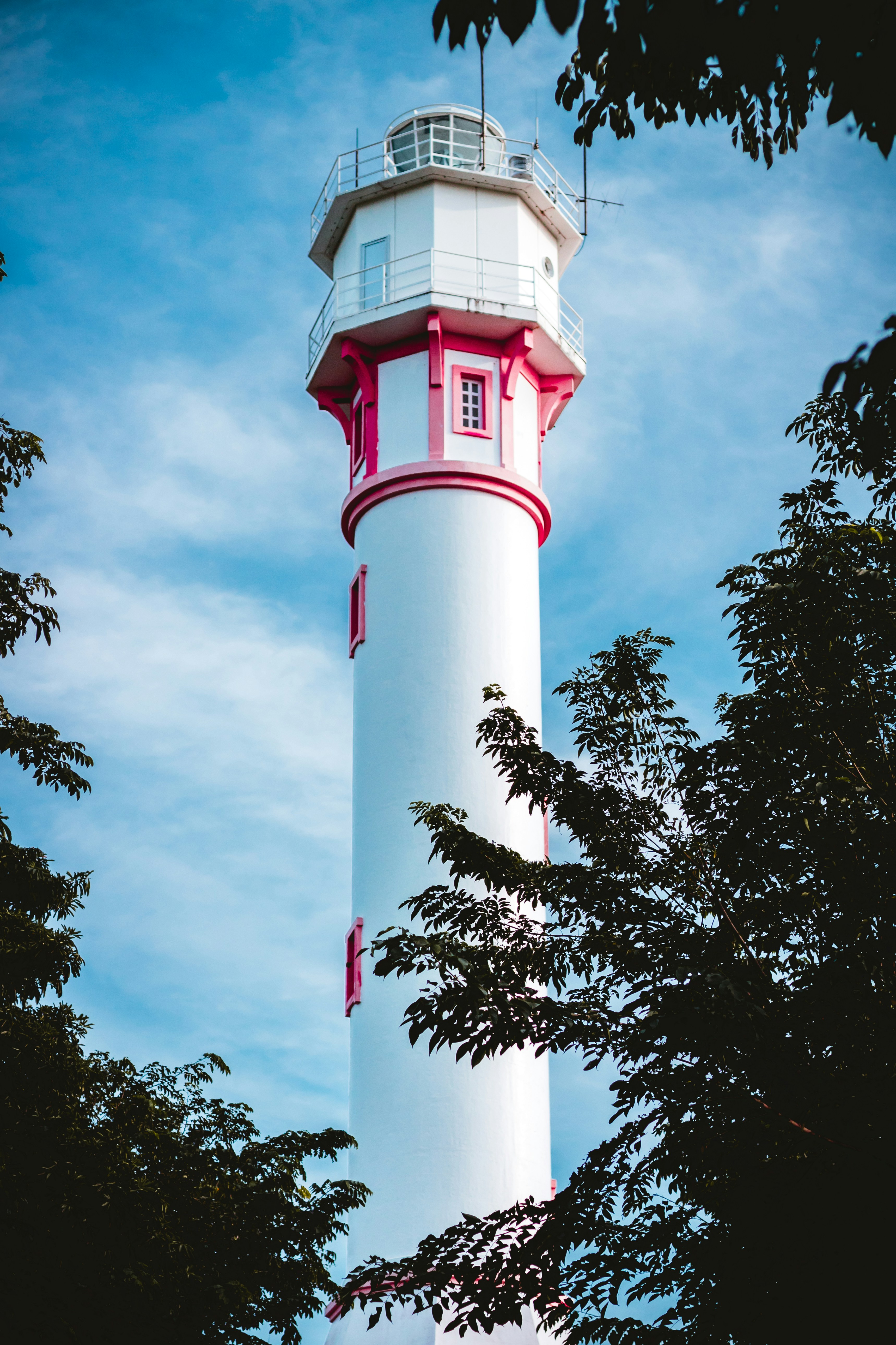 Colorful lighthouse surrounded by lush foliage under a clear blue sky.