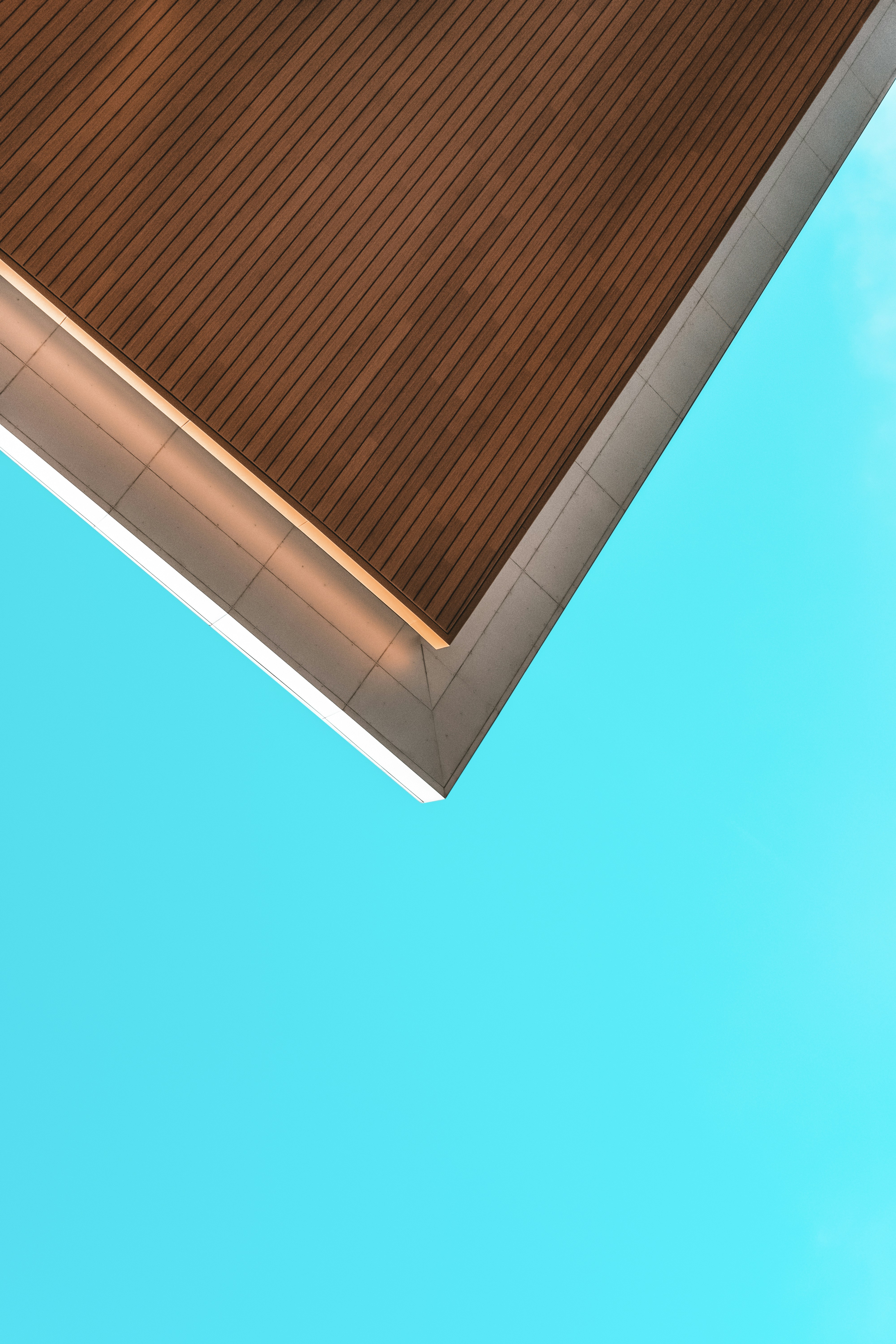 Stylish wooden deck meeting a crystal-clear pool under a bright sky. The design merges natural elements with modern aesthetics.