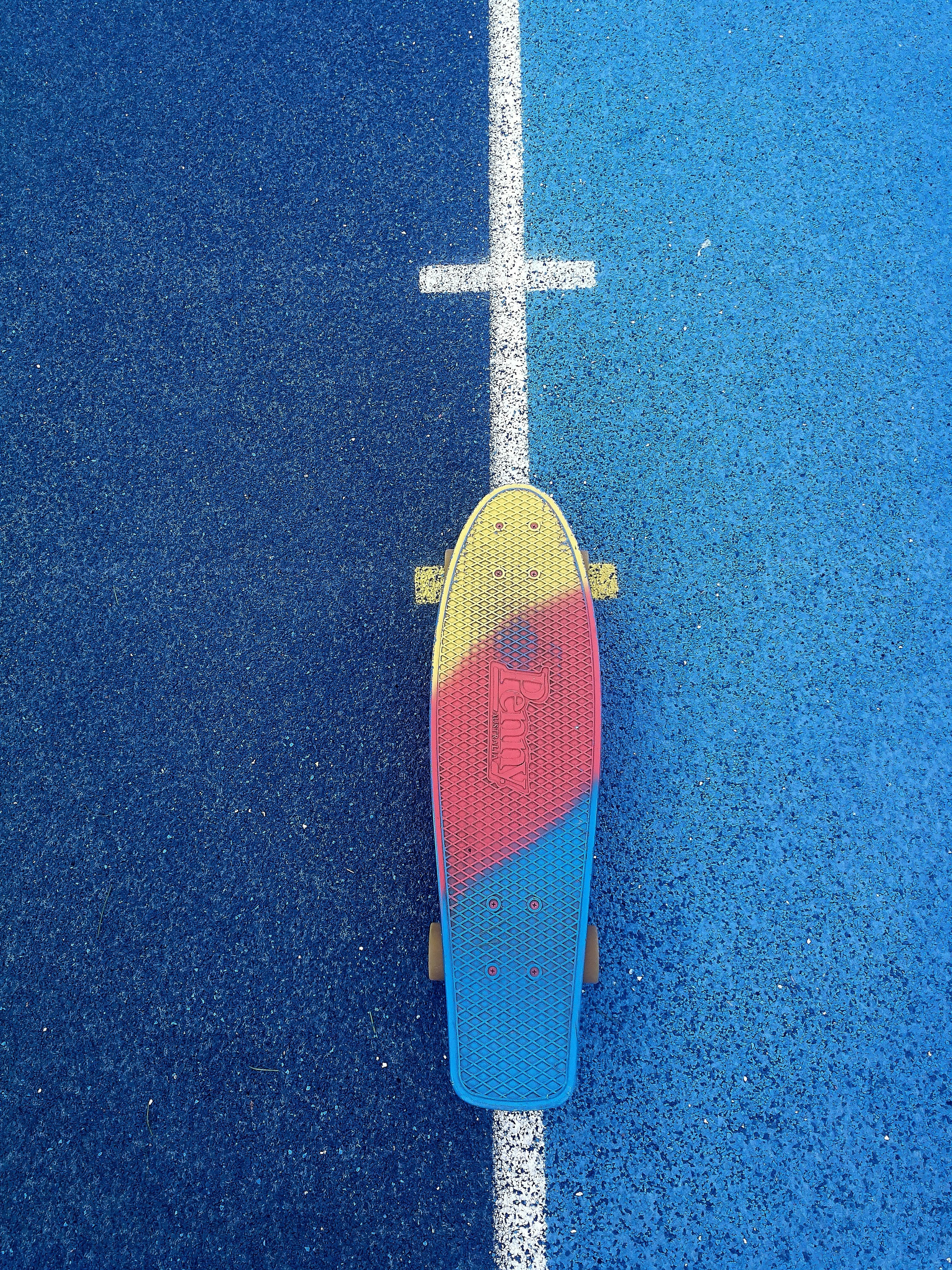 Colorful skateboard positioned on a blue and gray surface, highlighting the contrast between the two colors. The skateboard's unique design stands out against the background.