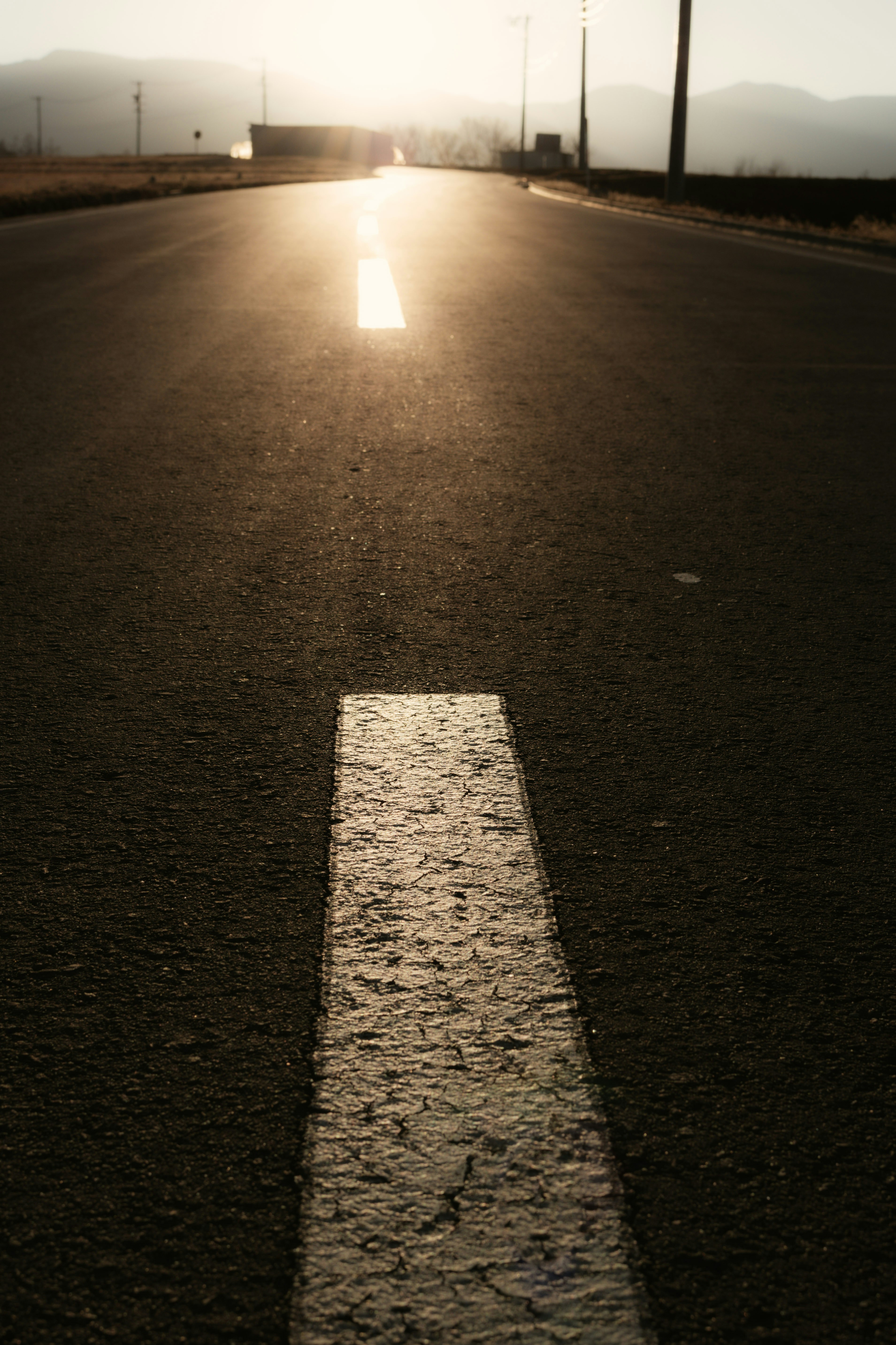 Sunset illuminating a deserted road with a prominent white lane marking leading toward the horizon.
