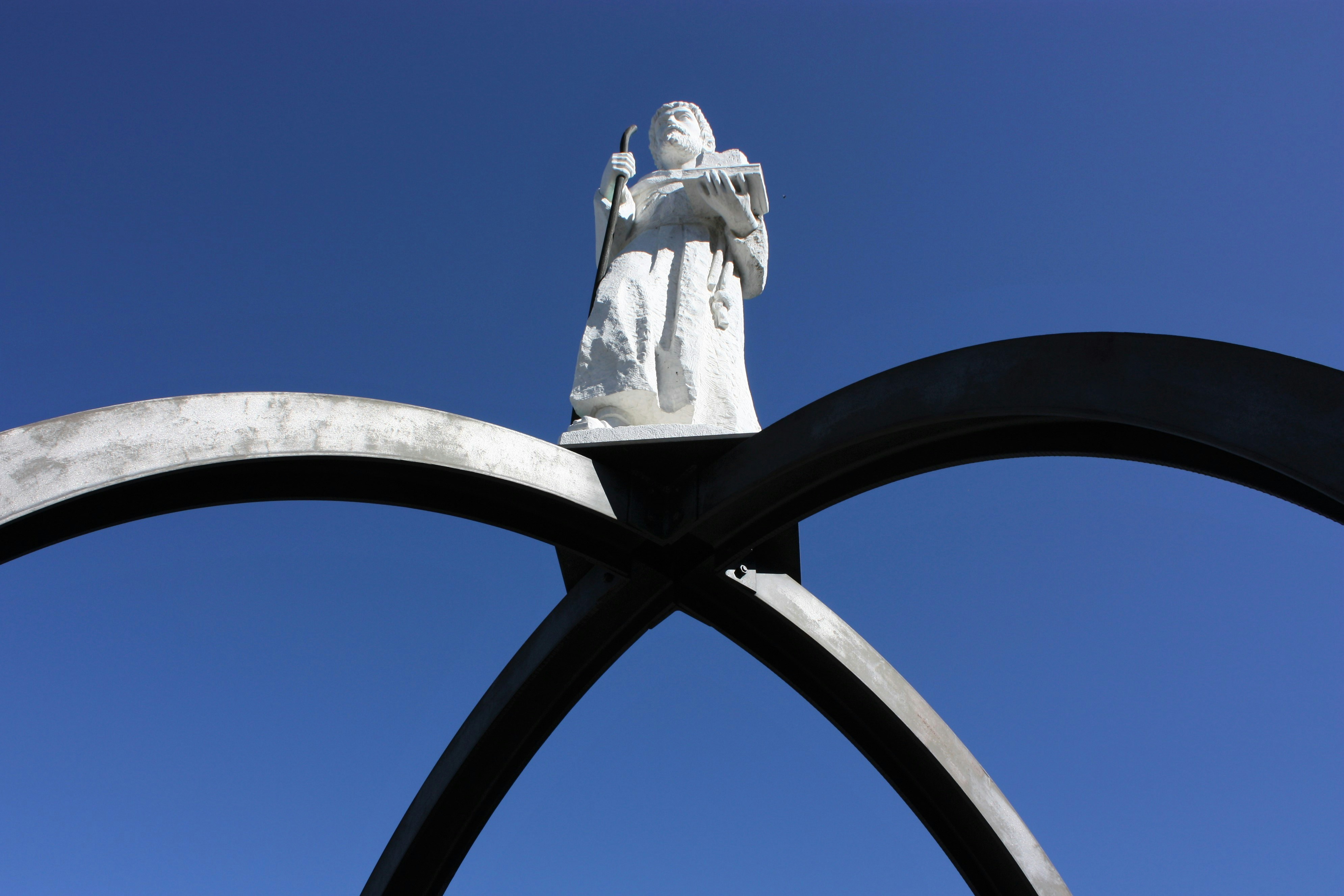 Stone Scholar atop Circling Arches Against a Clear Blue