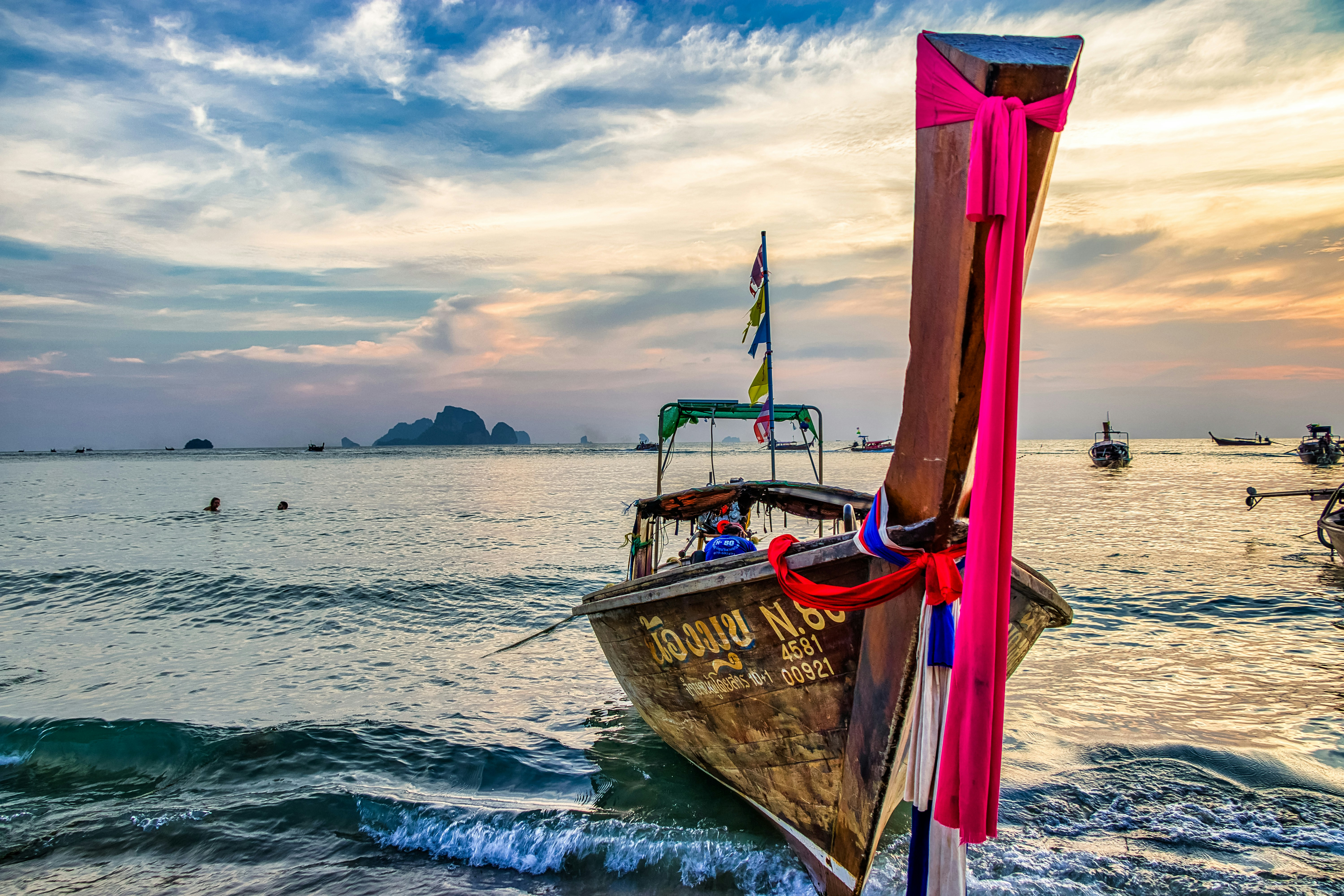 Colorful longtail boat anchored by the shore against a backdrop of a tranquil sea and a vibrant sunset sky.