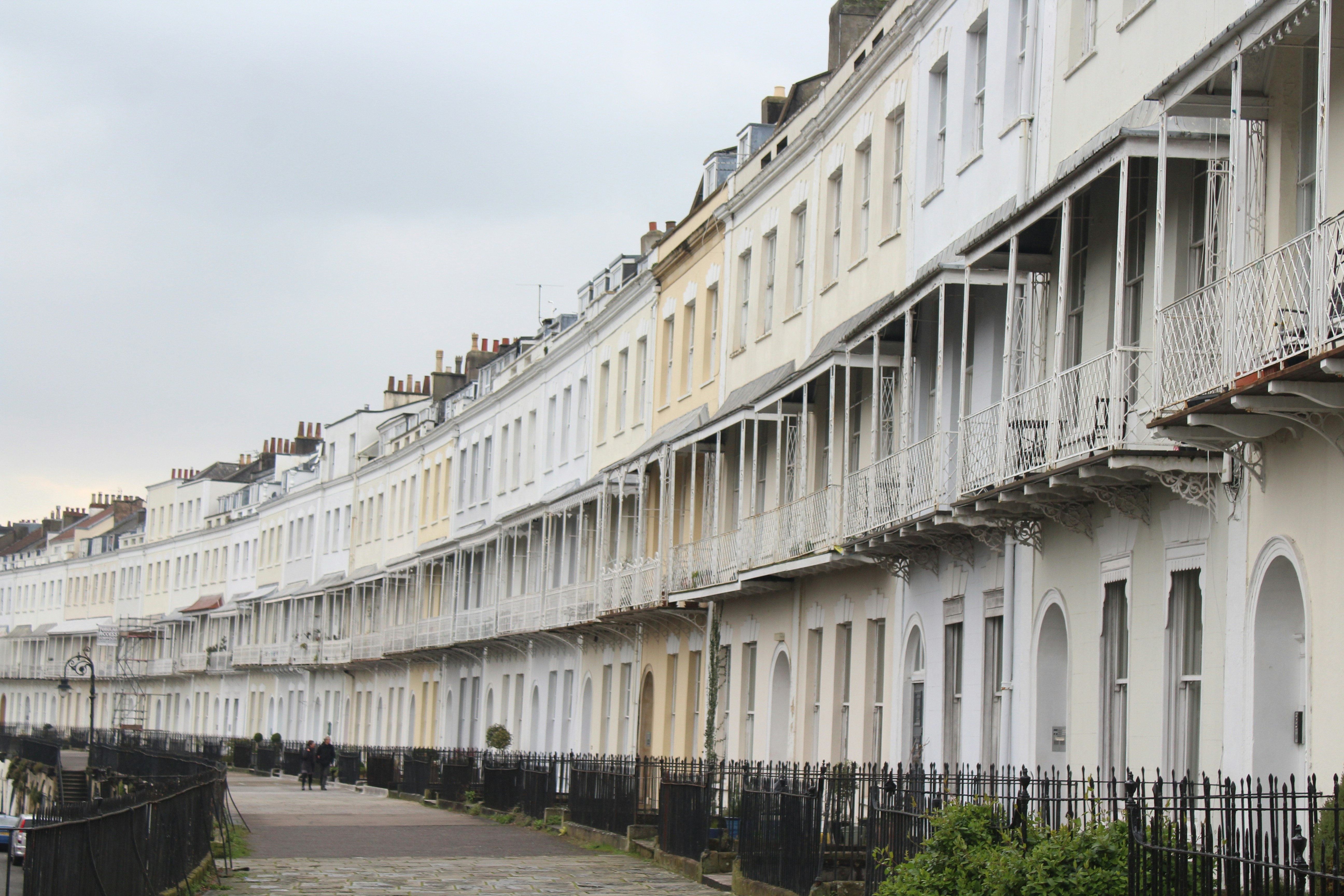 Curved row of historic terraced houses with white facades and iron railings under a cloudy sky.