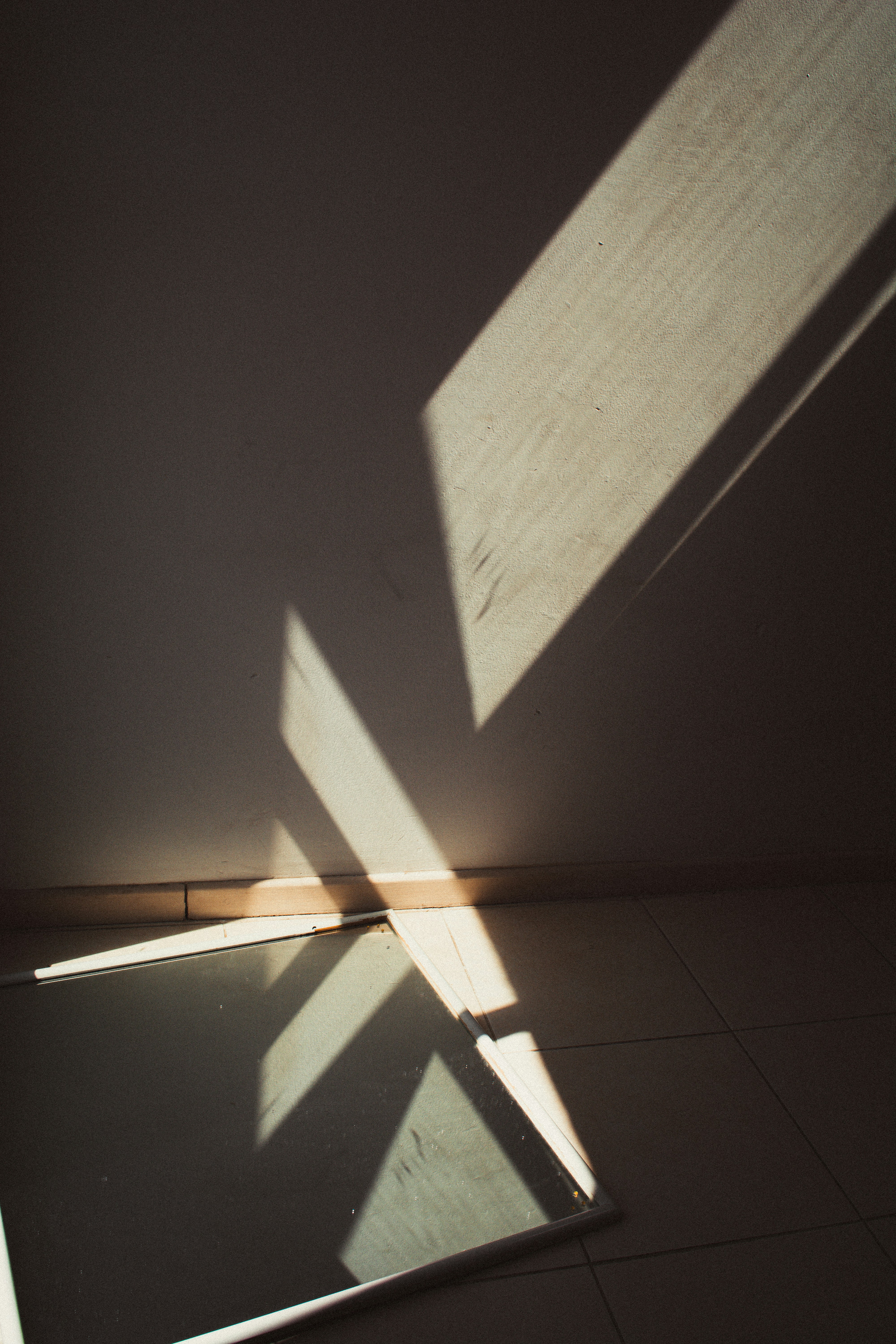 Diagonal shadows cast on a wall and floor create an abstract composition, emphasizing the interplay of light and reflection.