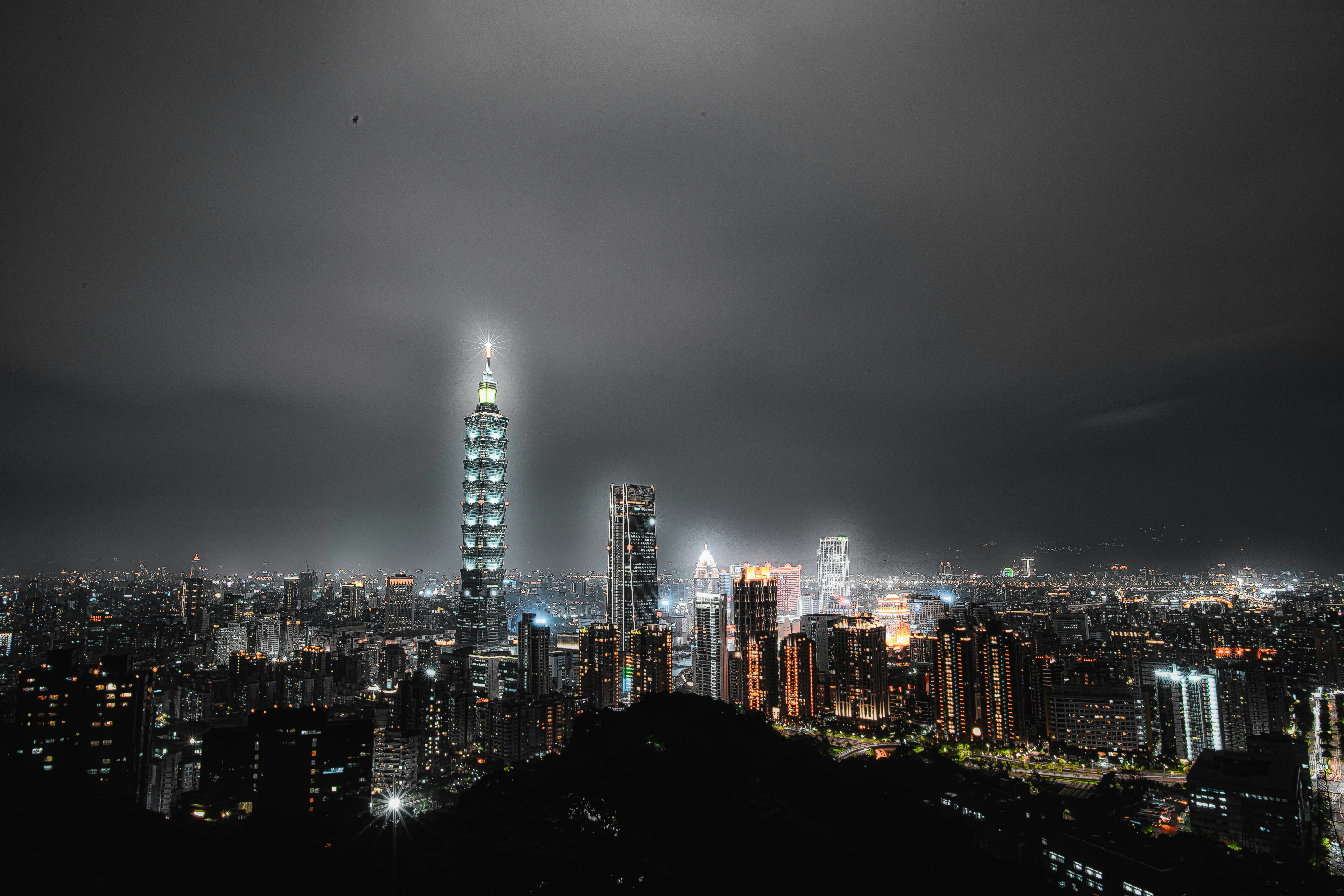 City skyline at night with skyscrapers illuminated under a cloudy sky.