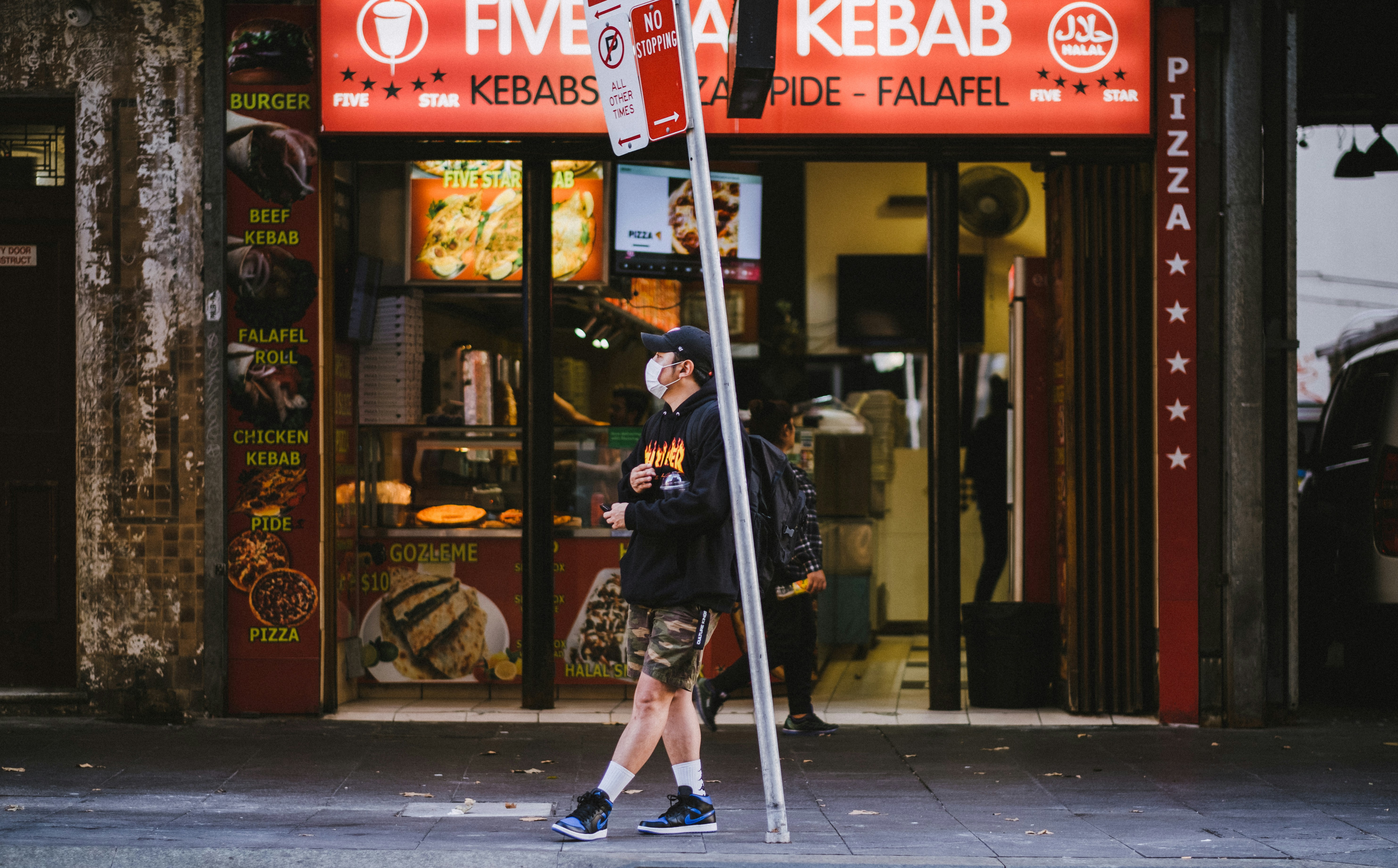 Mask and neon: a quiet pause by a kebab storefront