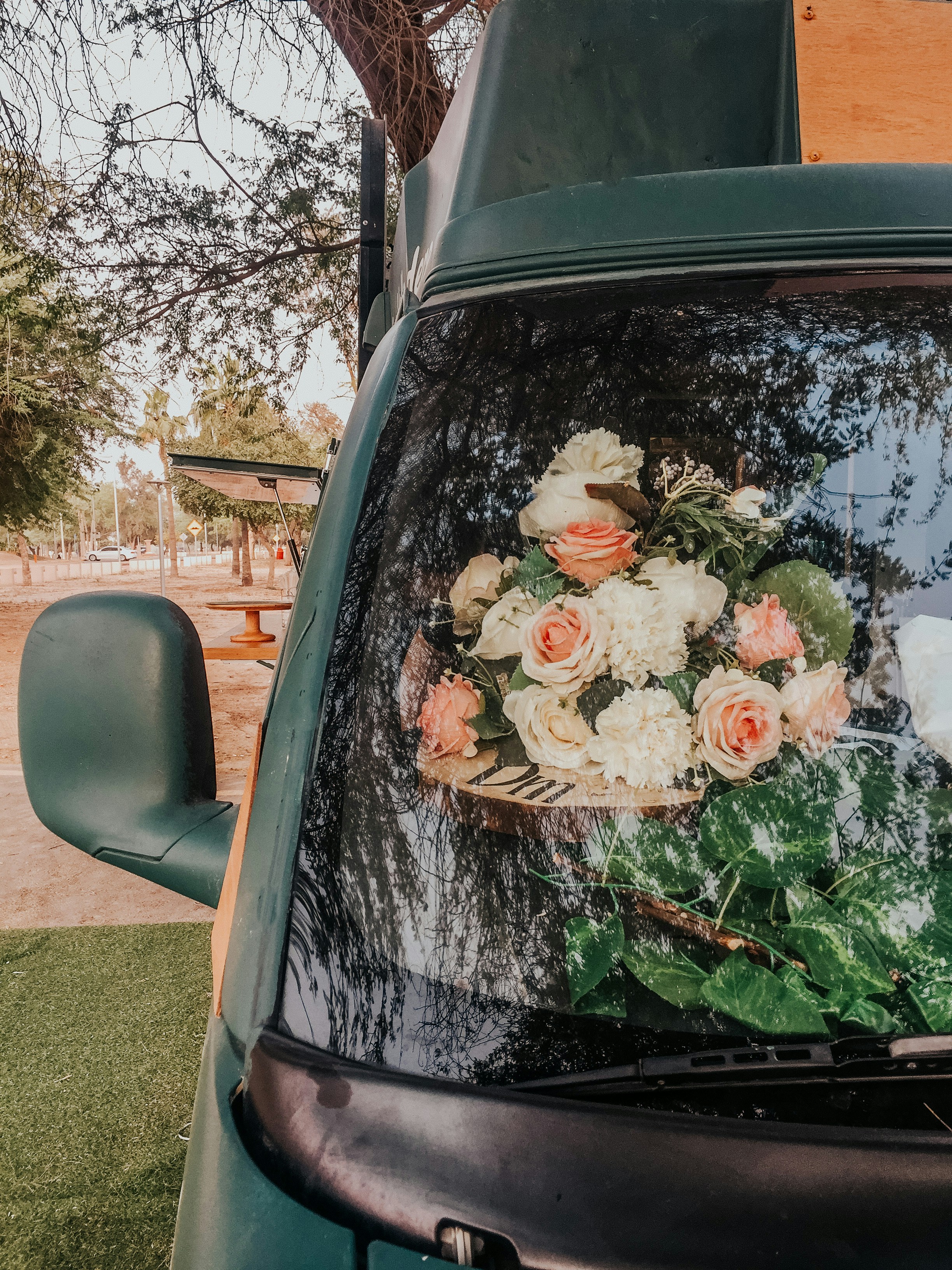 A vintage van adorned with a beautiful arrangement of pastel flowers and greenery displayed on its windshield.