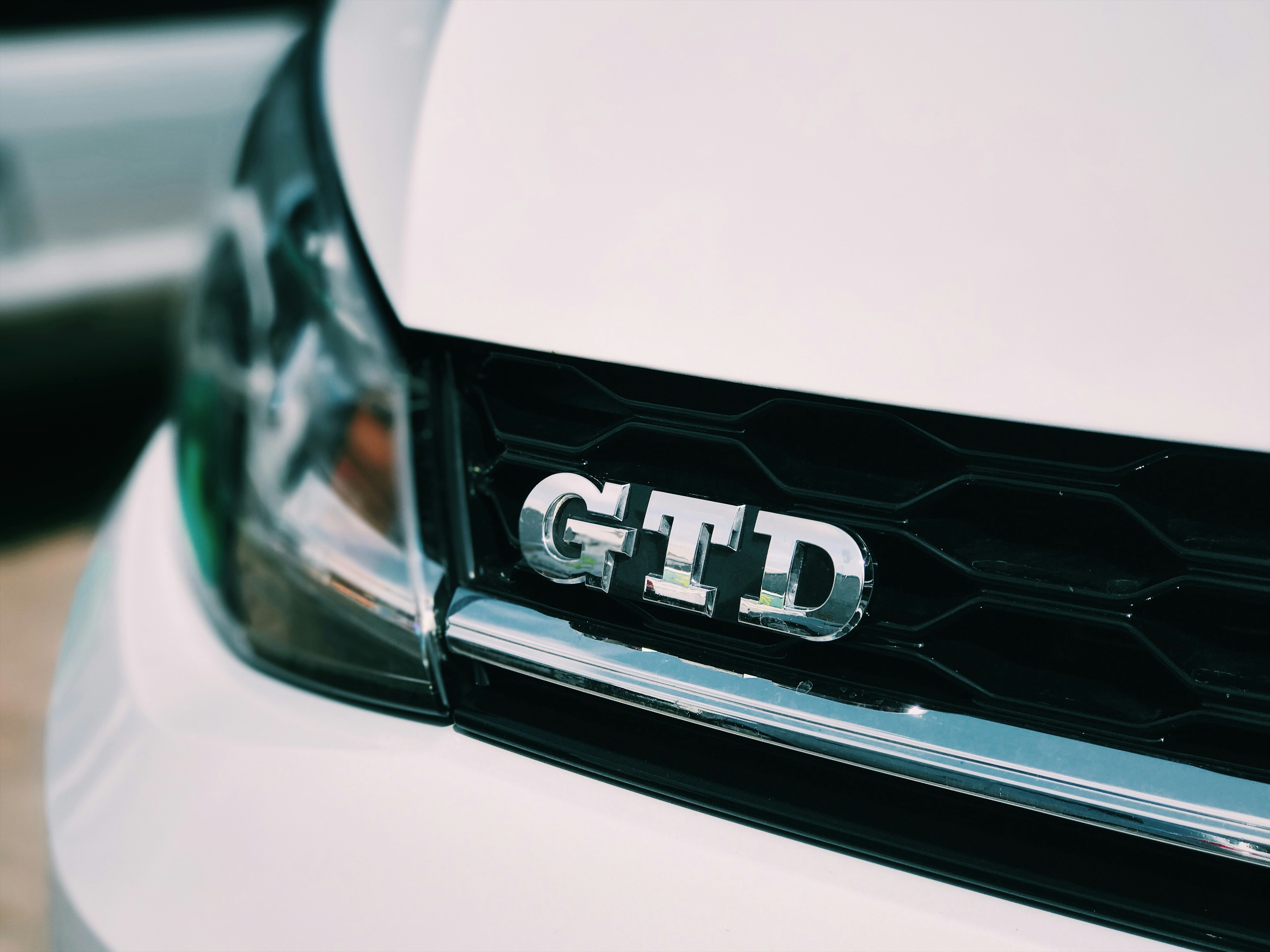 Close-up of a Volkswagen GTD badge on a white car, highlighting the car's sleek grille and glossy finish.