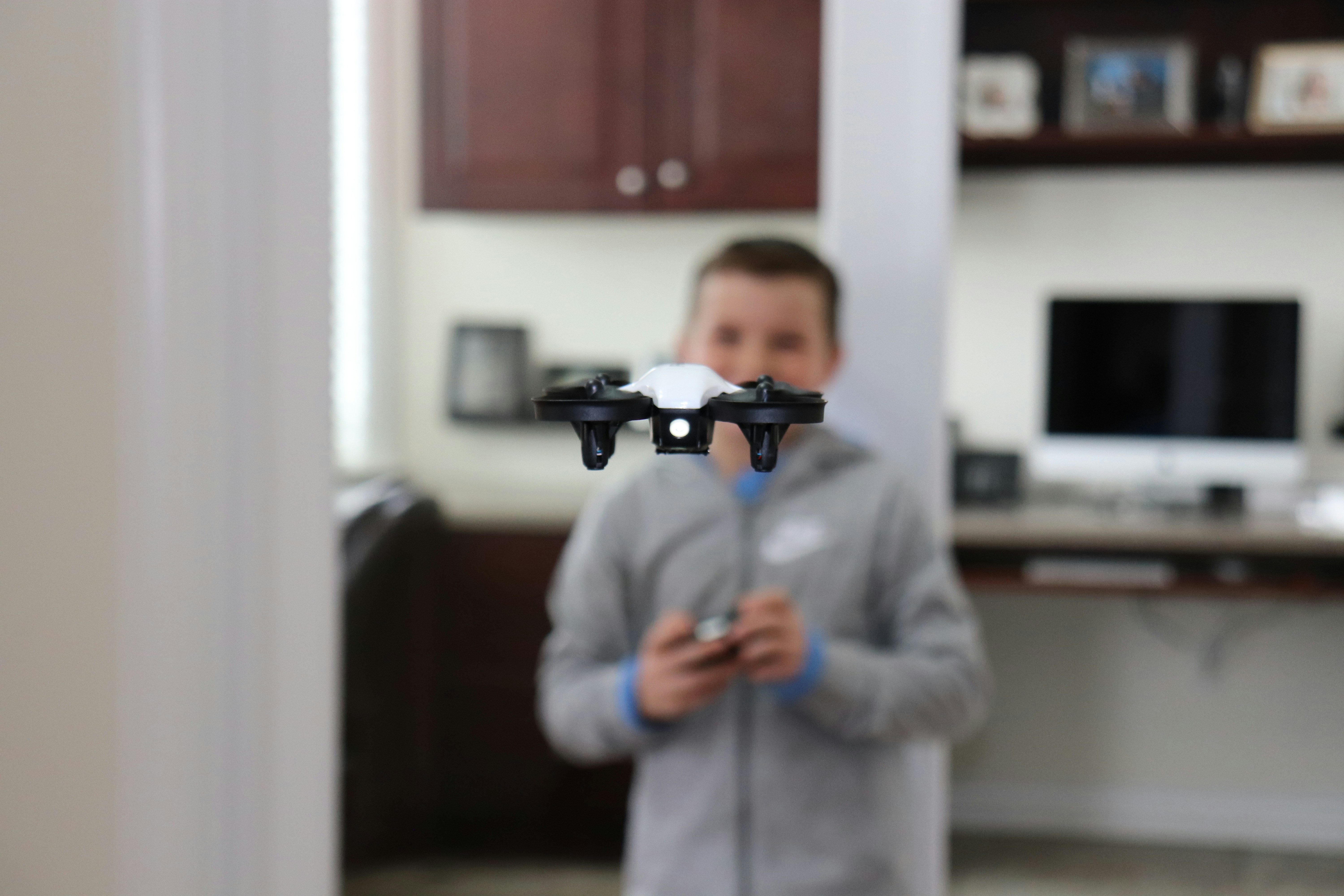 A drone hovers mid-air, controlled by a young boy in a cozy indoor setting, showcasing the blend of technology and play.