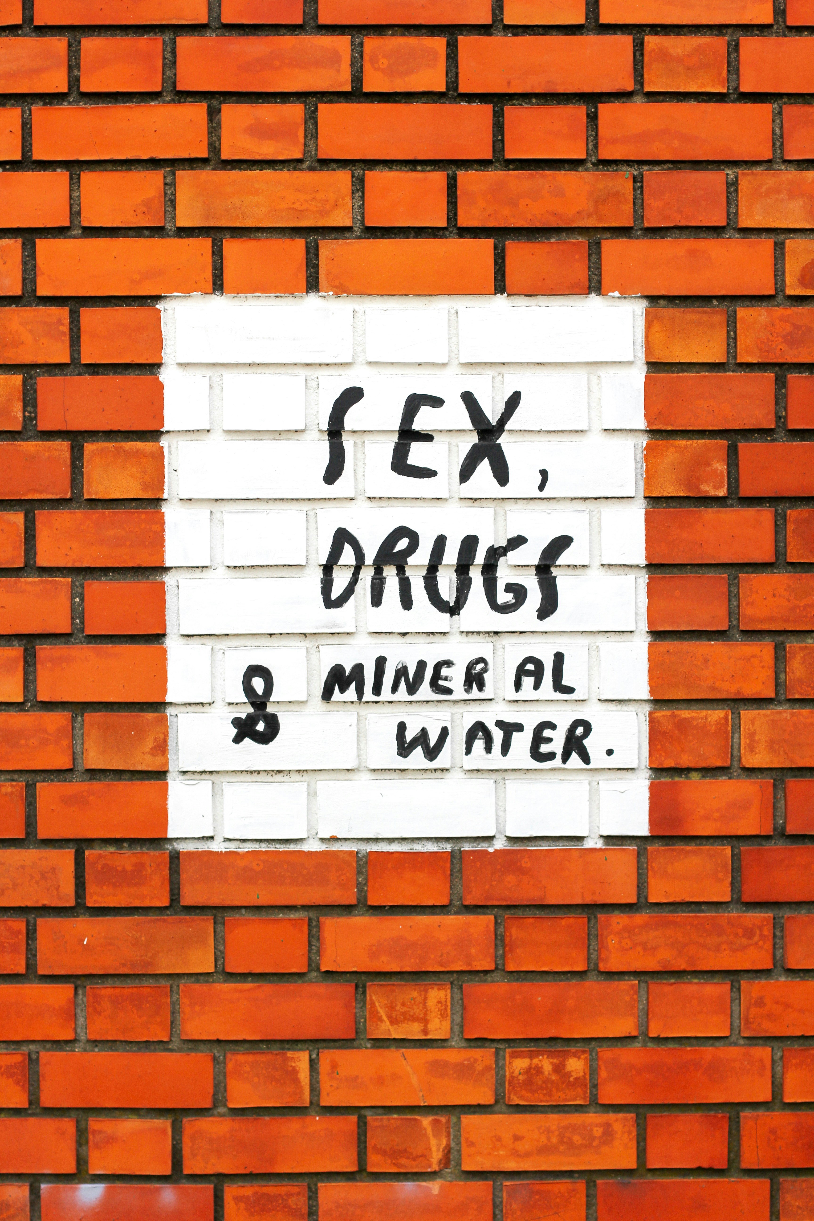 Graffiti on a brick wall featuring bold text that reads 'SEX, DRUGS & MINERAL WATER.' emphasizing a juxtaposition of themes.