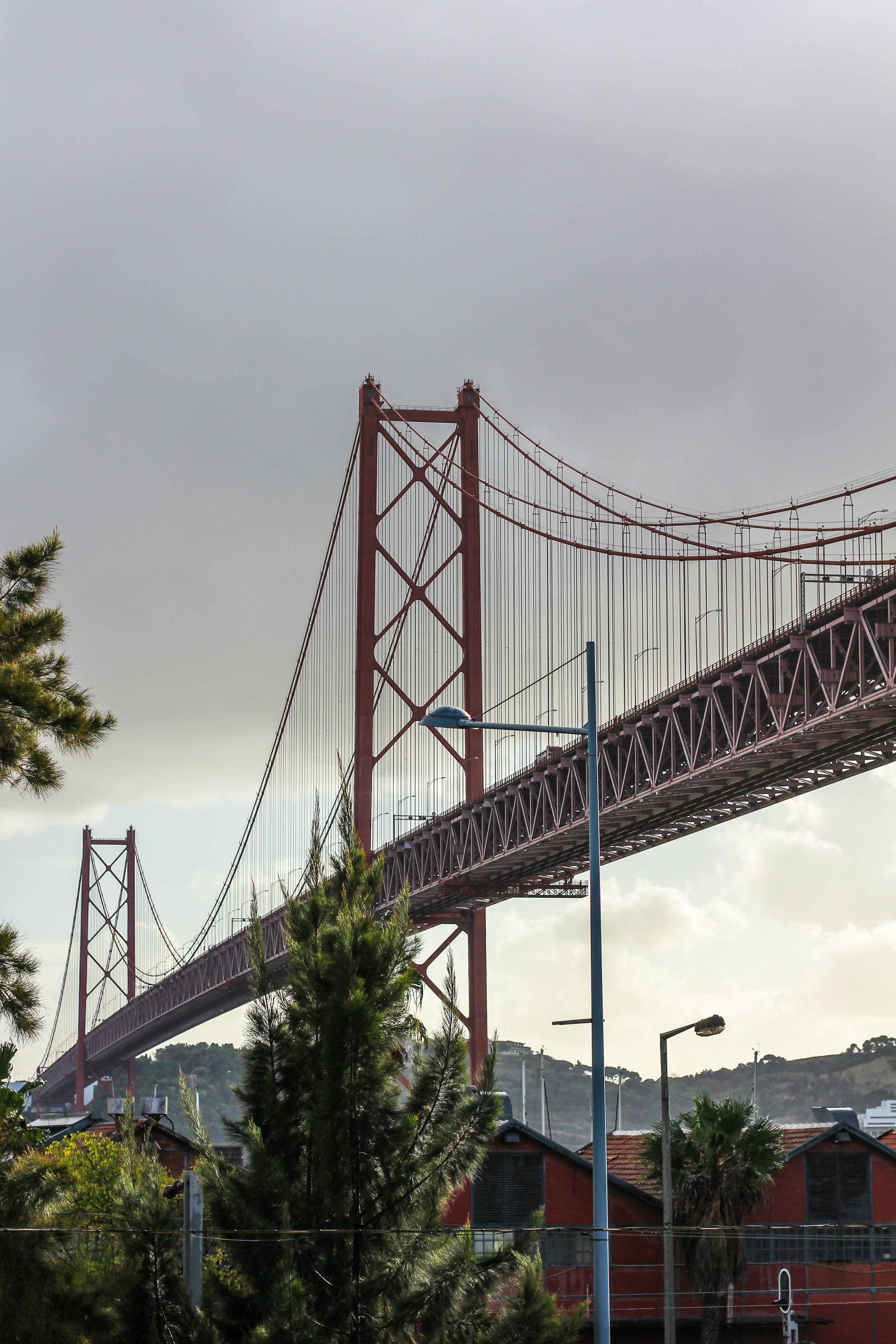 Crimson Suspension Bridge Rising Above a Quiet Coastal Village Under an Overcast Sky
