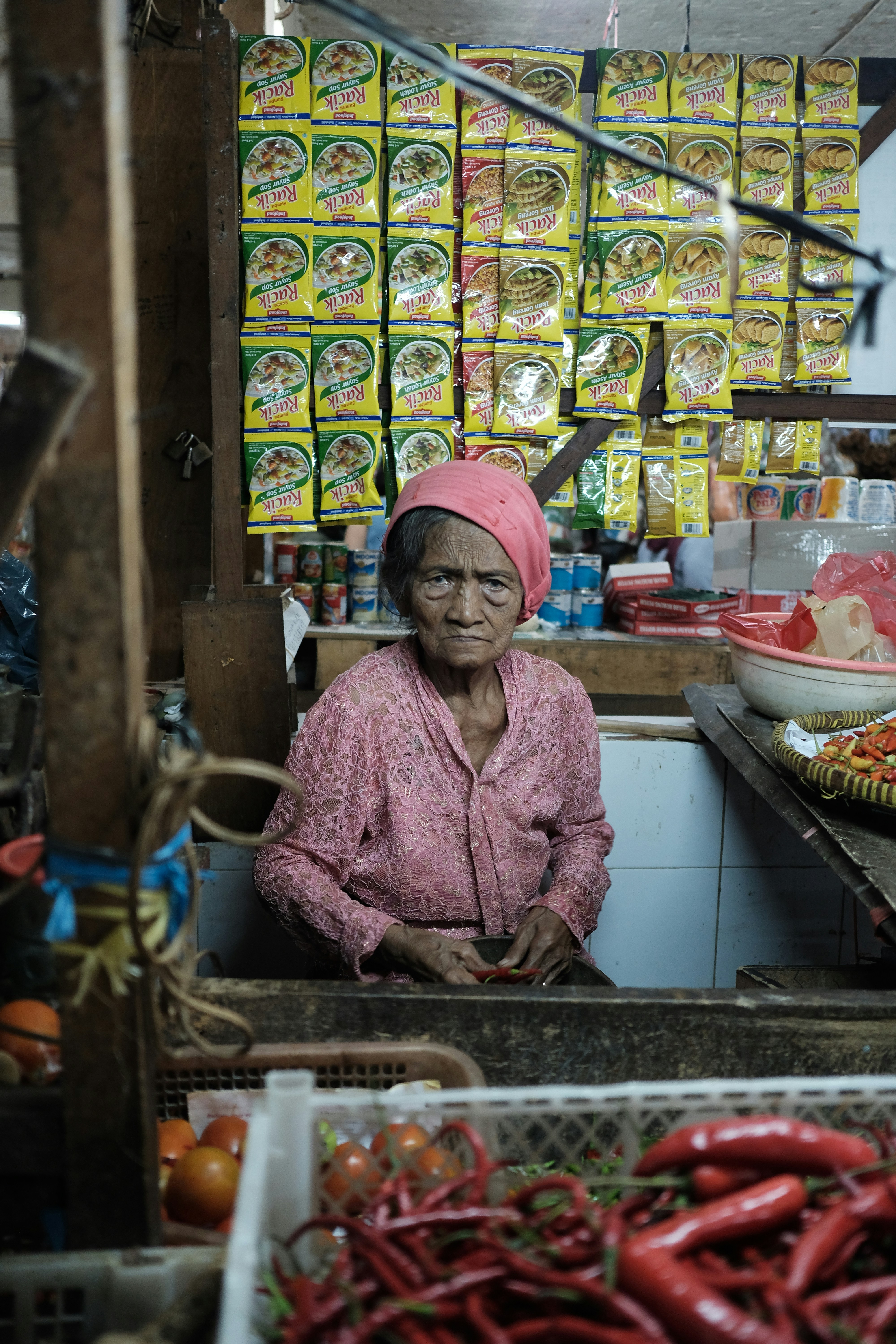 an old woman sell the groceries in traditional market | woman in pink hijab sitting on chair