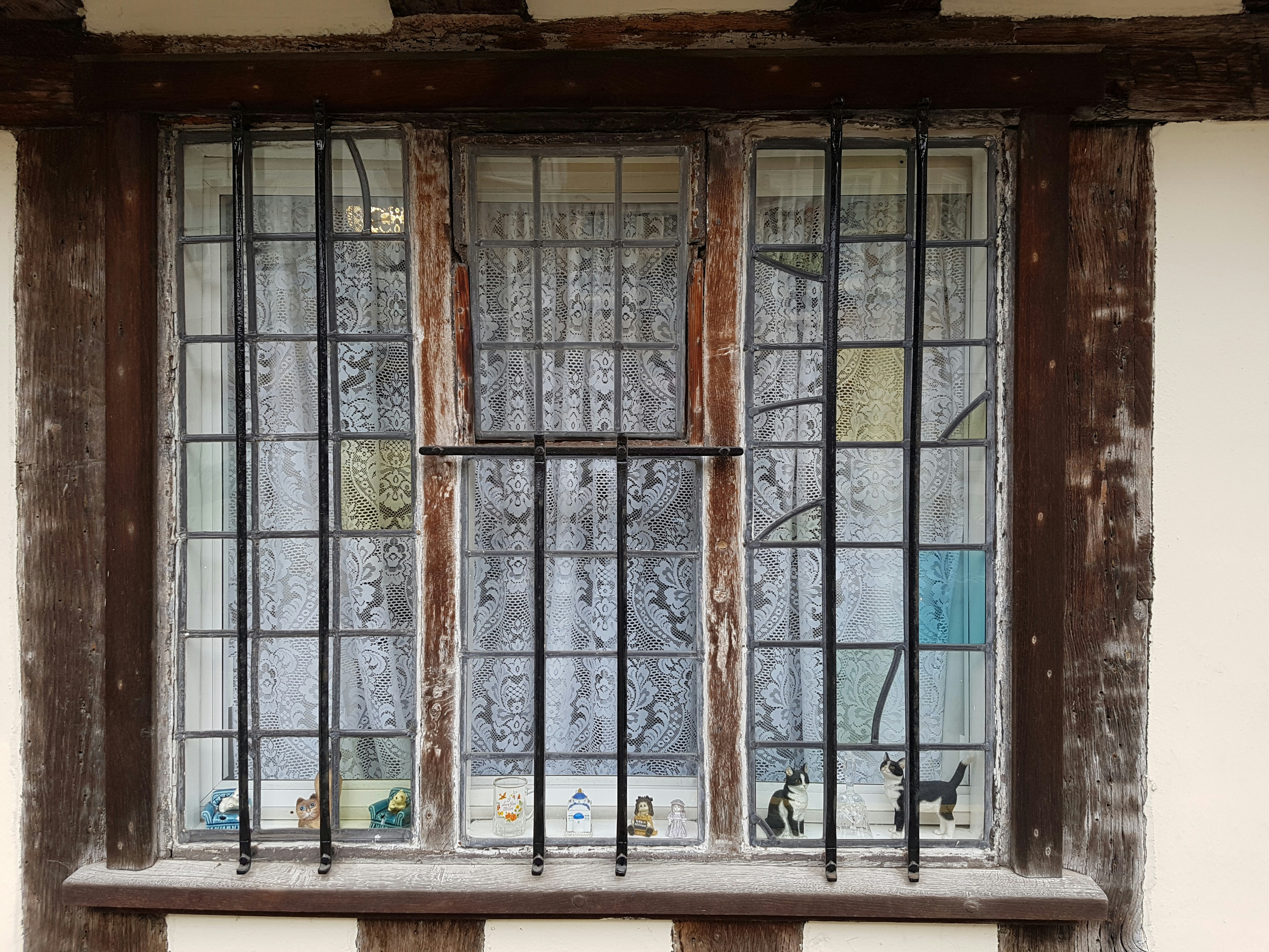 A weathered wooden window with metal bars, showcasing textured glass panes and subtle colored accents.