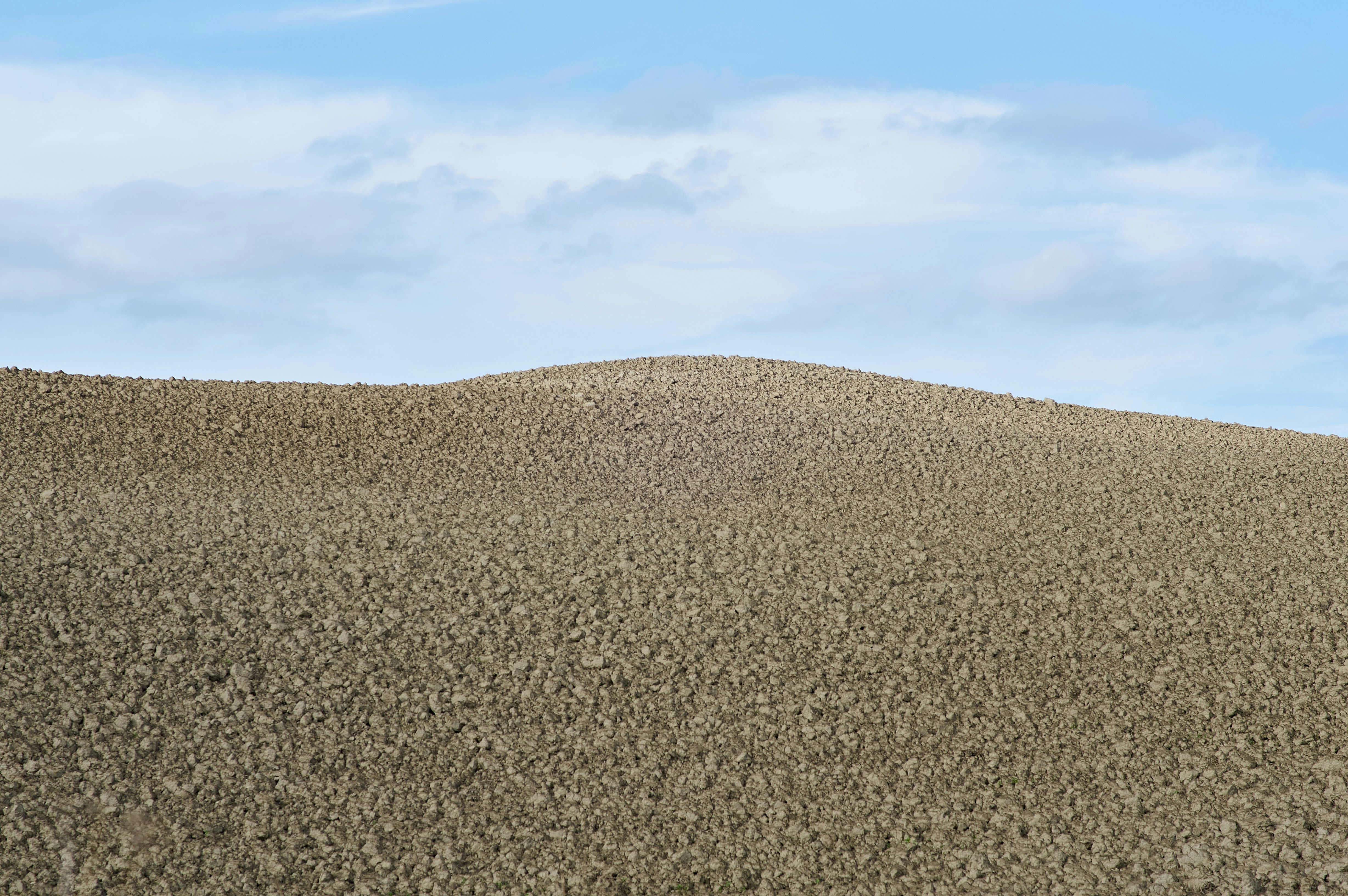 Pebble-Dusted Crest: A Dune's Quiet Curve Under a Clear Sky